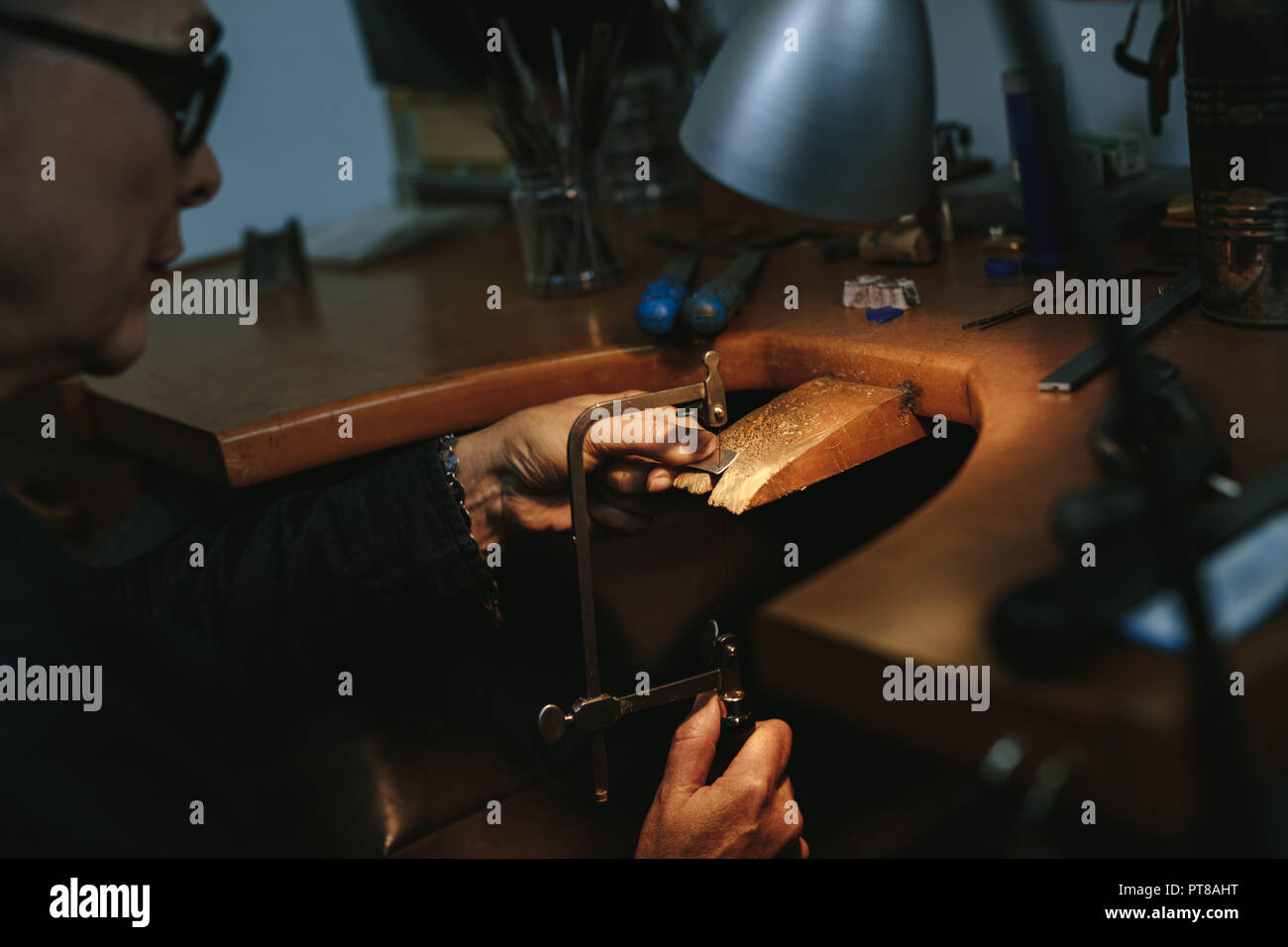 Female jewelry maker cutting metal with a band saw on workbench at ...