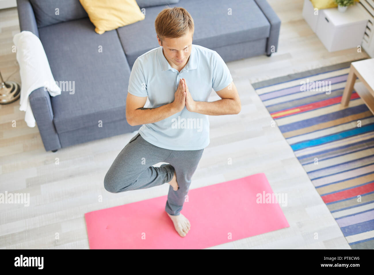 Active guy practicing yoga exercises on pink mat by sofa in living-room ...