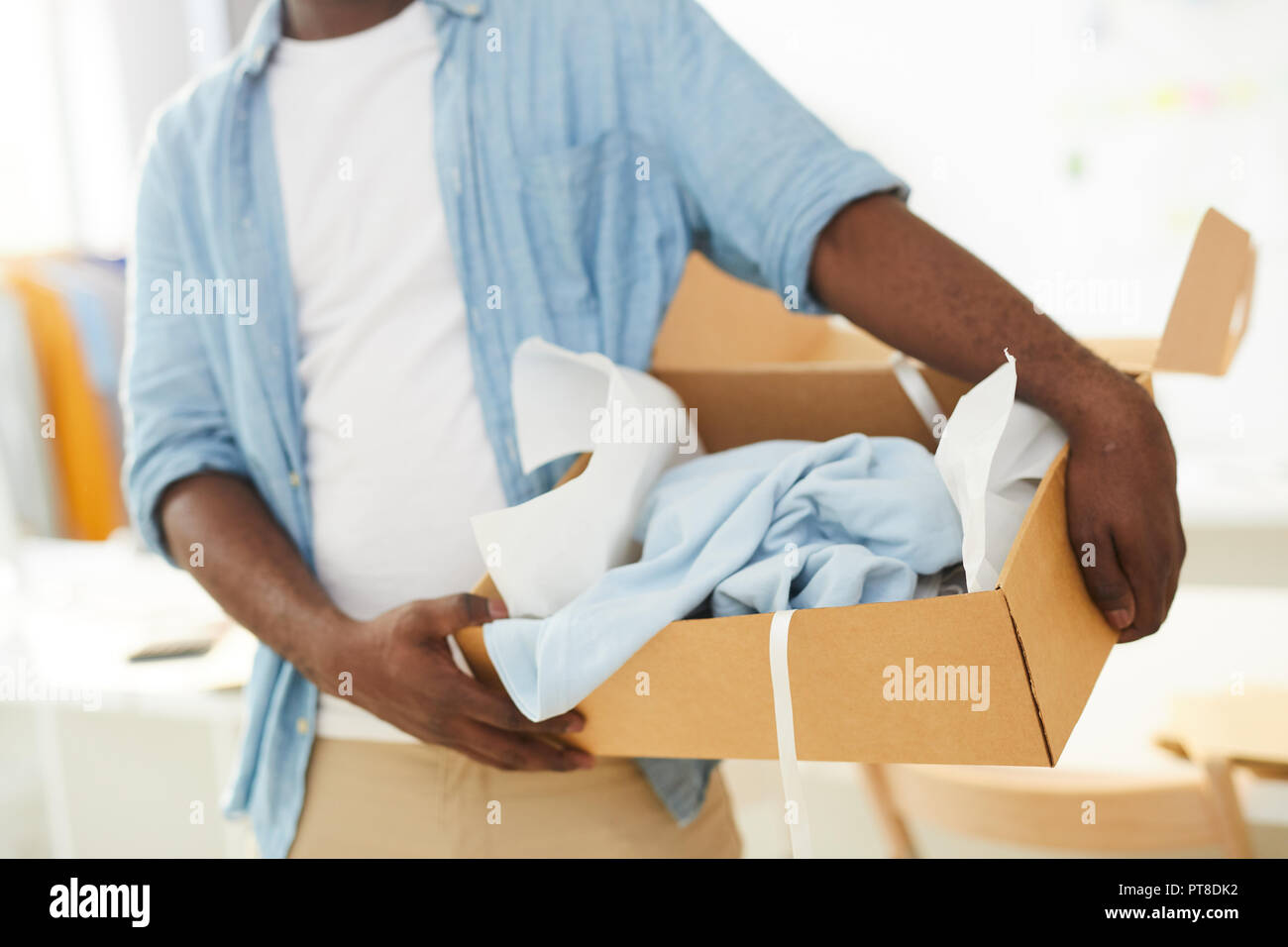 Young man carrying open carton box with folded clothes while working in ...