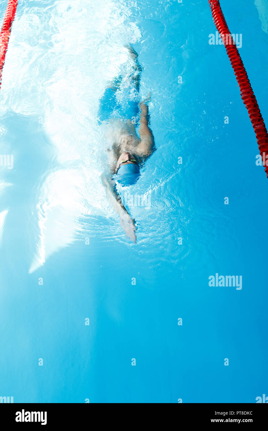 Photo on top of young sporty man in blue cap swimming on back in ...