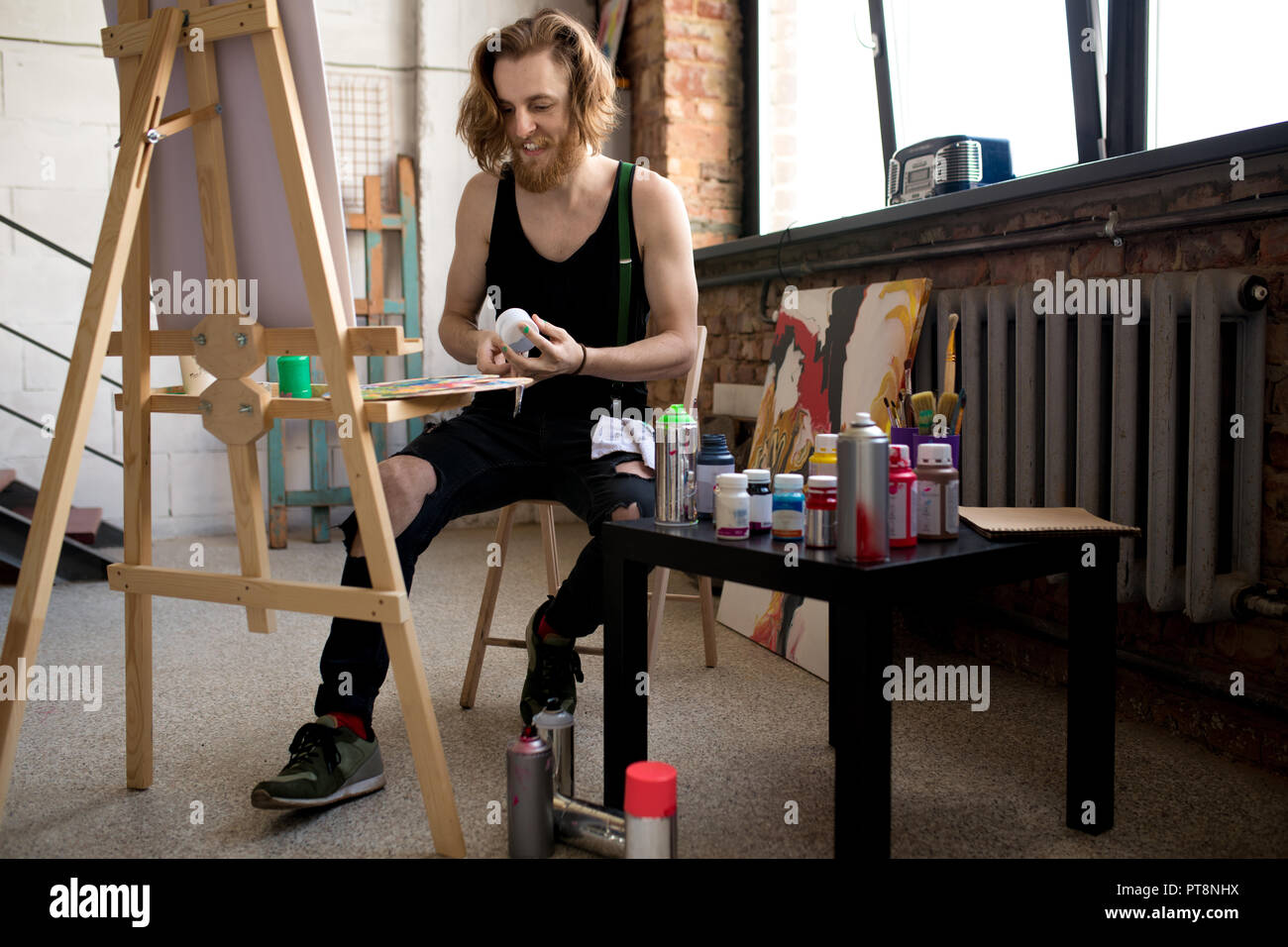 Full length portrait of handsome long haired artist painting on easel ...