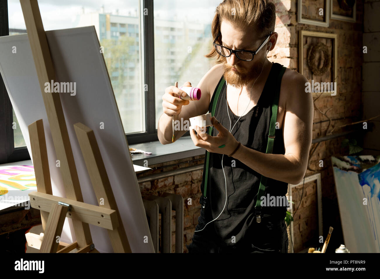 Waist up portrait of contemporary long haired artist painting pictures ...