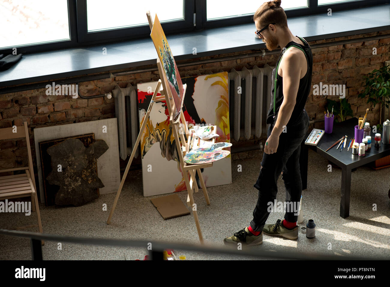 Full length portrait of contemporary long haired artist looking at ...