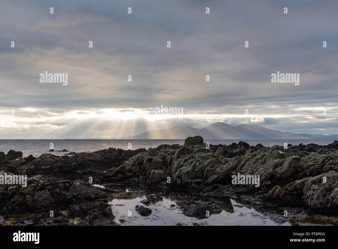 Crepuscular rays over Mourne Mountains and Irish Sea and rock pool in ...