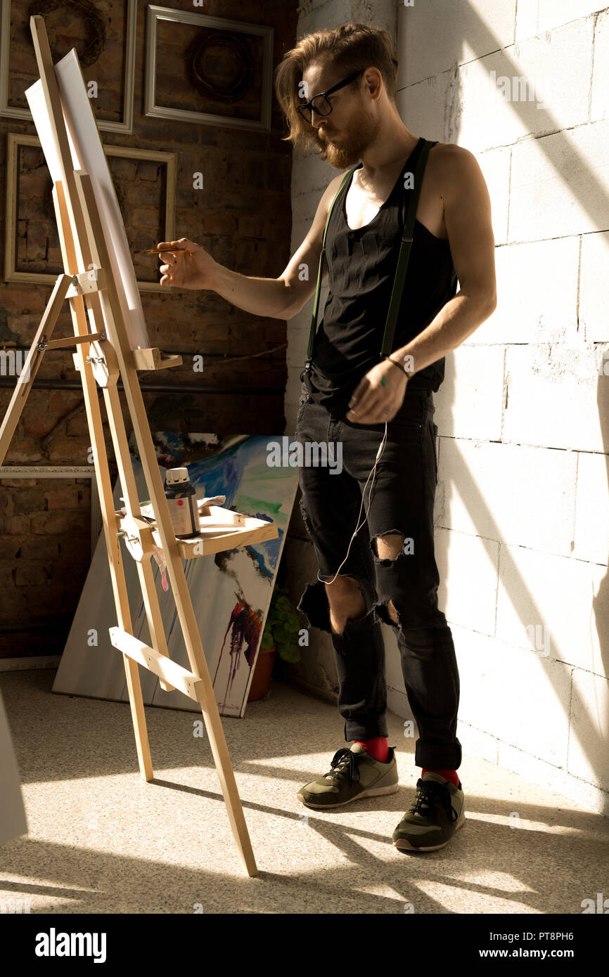 Full length portrait of handsome male artist painting picture on easel ...