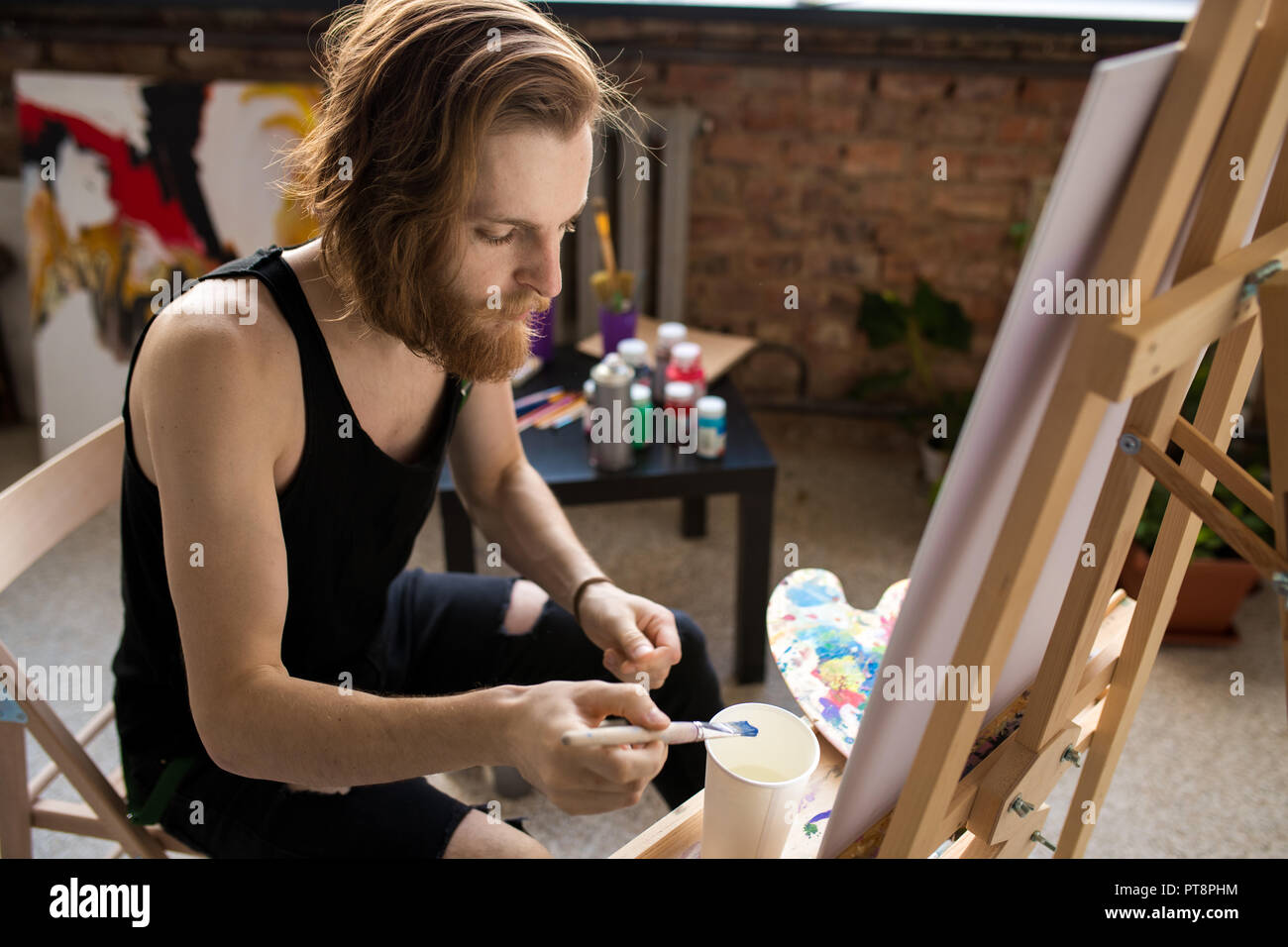 Portrait of contemporary long haired artist mixing watercolor paints ...