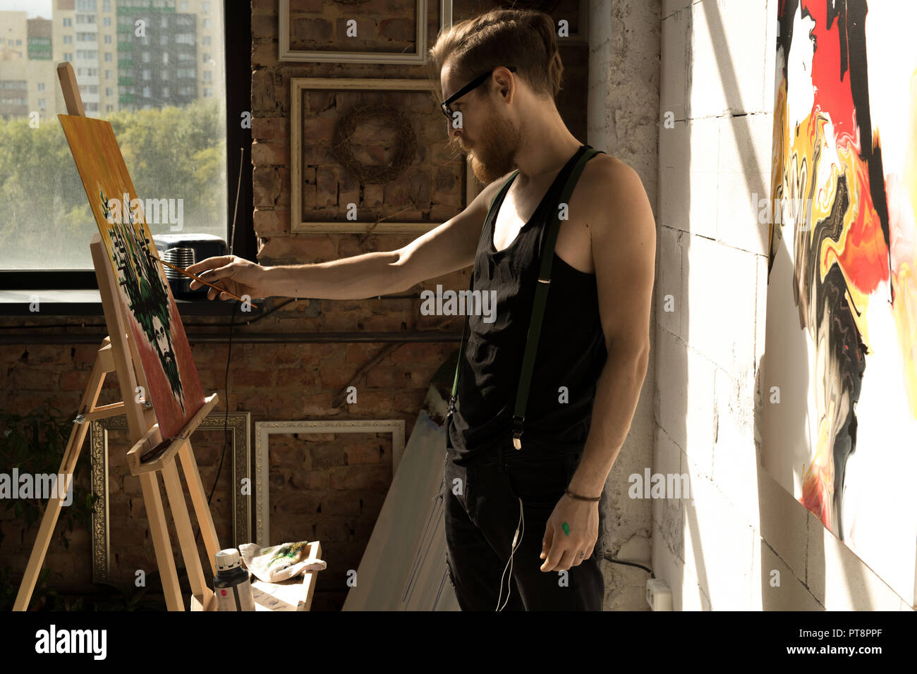 Side view portrait of handsome male artist painting picture on easel in ...