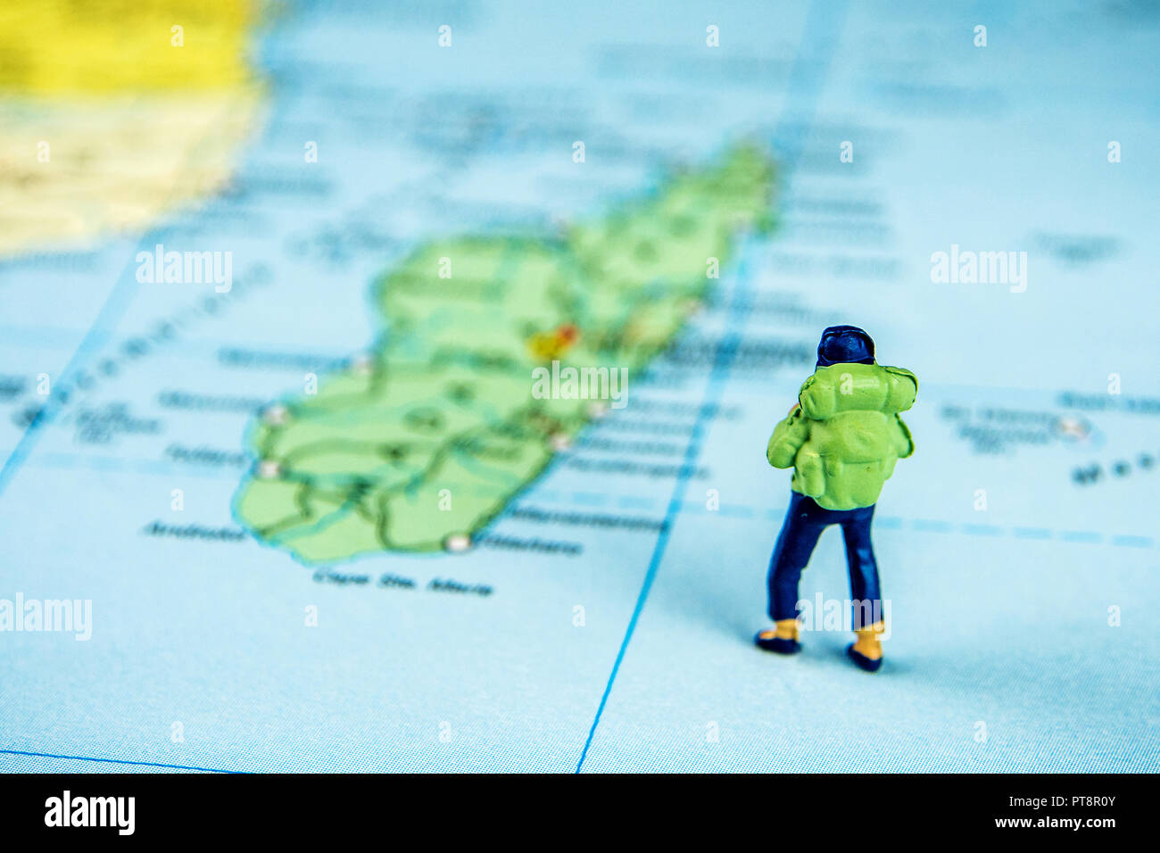 closeup of miniature figurine of young traveller standing on big map ...