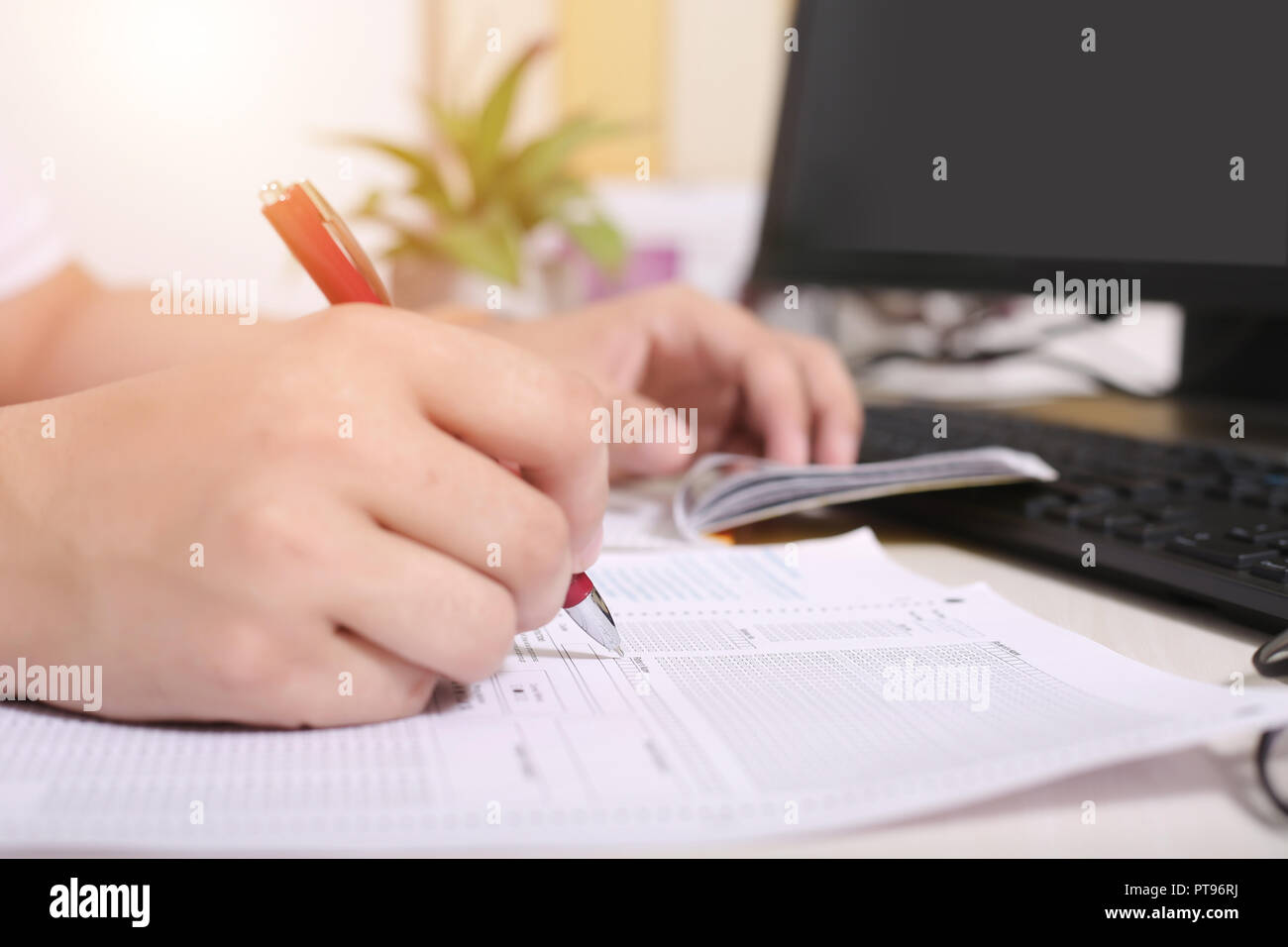 Man is filling sheet with pen. Picture of computer, keyboard and ...