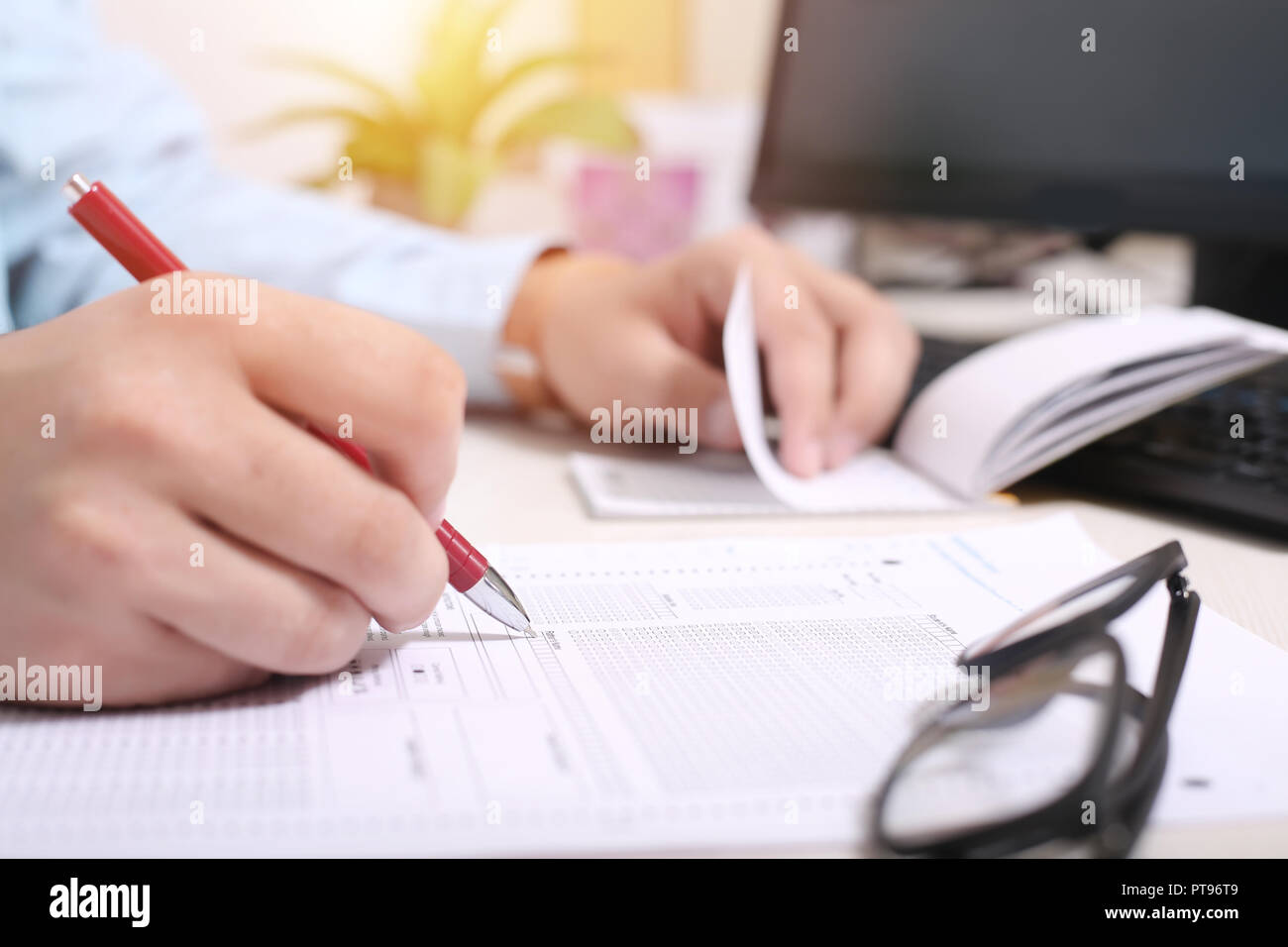 Man is filling sheet with pen. Picture of computer, keyboard, glasses ...