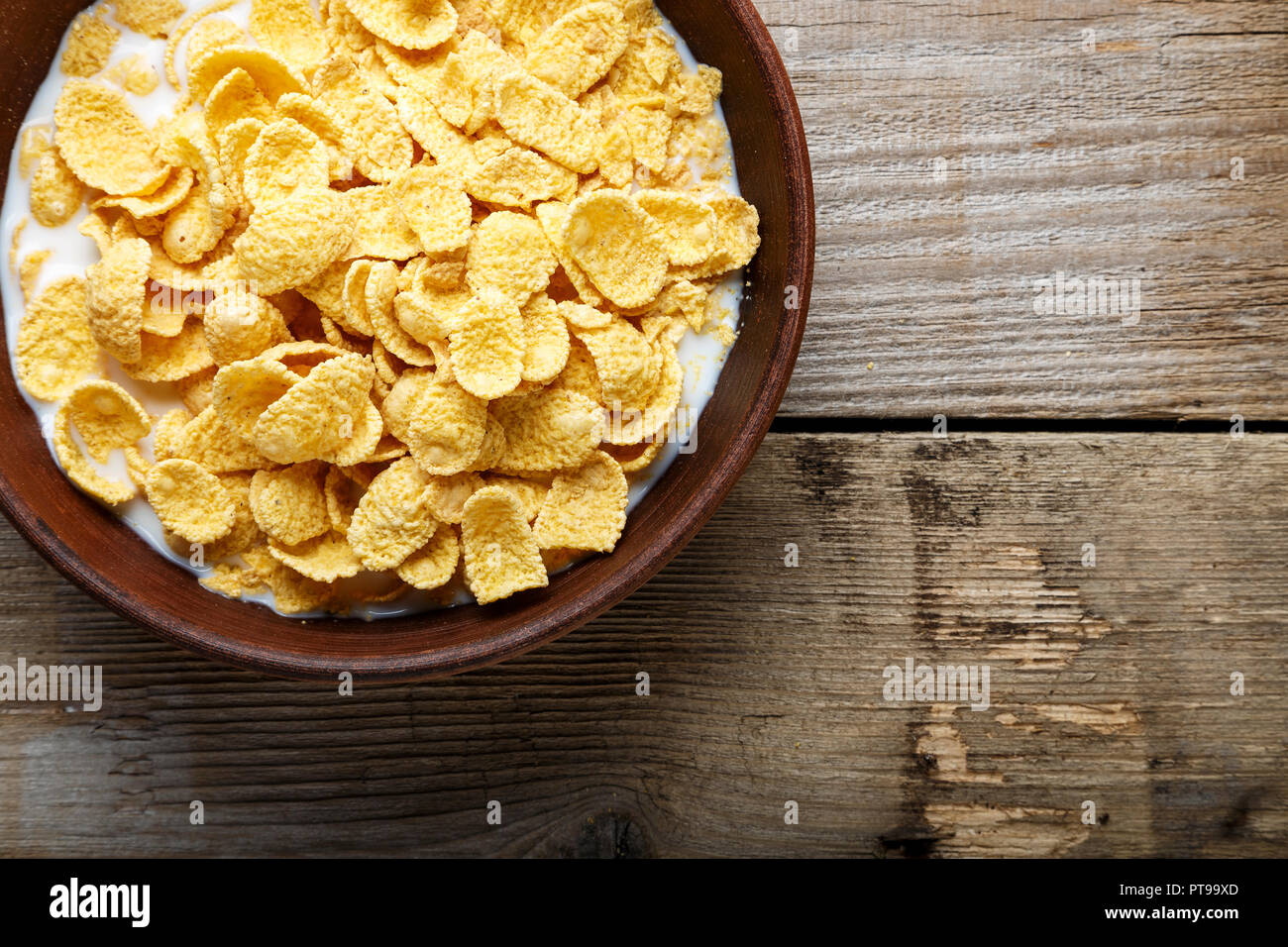 flakes of cereals with milk in a clay plate on a brown wooden ...