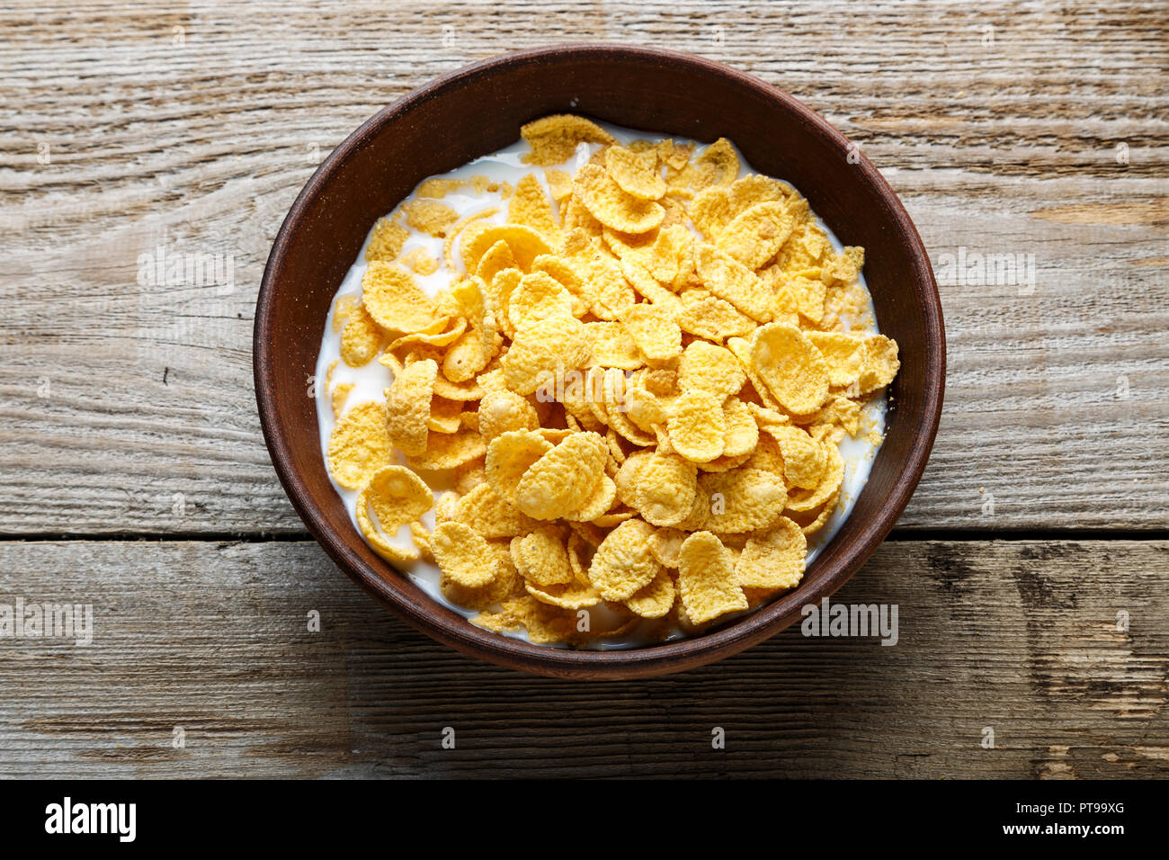 flakes of cereals with milk in a clay plate on a brown wooden ...