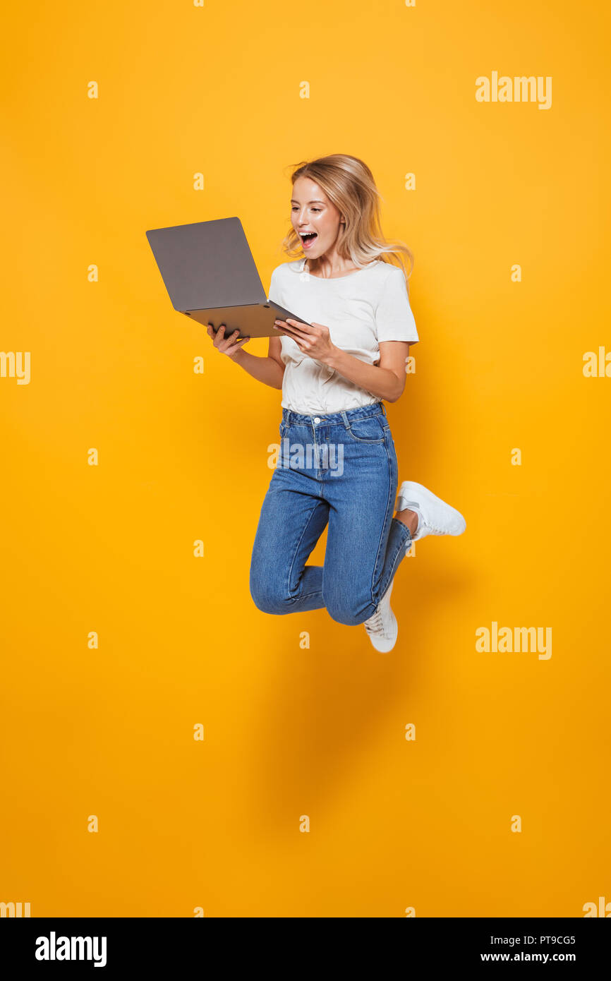 Photo of happy excited young woman jumping isolated over yellow wall ...