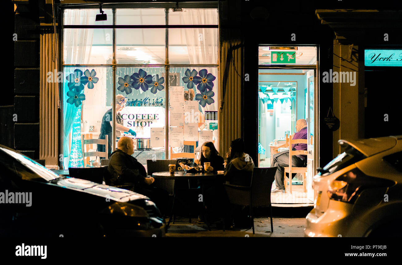 Tourists drinking coffee outside a coffee shop in Matlock at night time ...