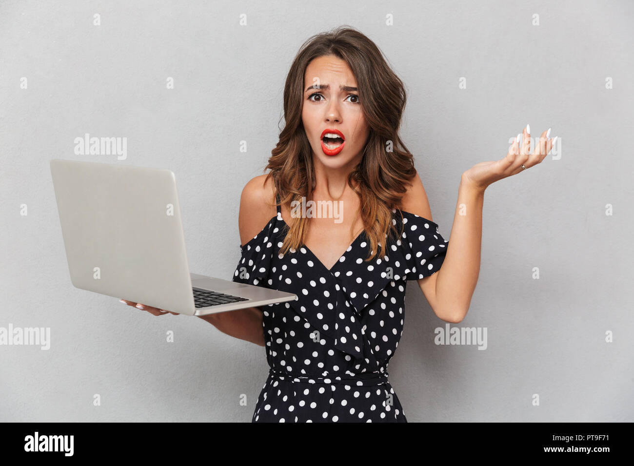 Portrait of a puzzled young girl in dress over gray background, holding ...