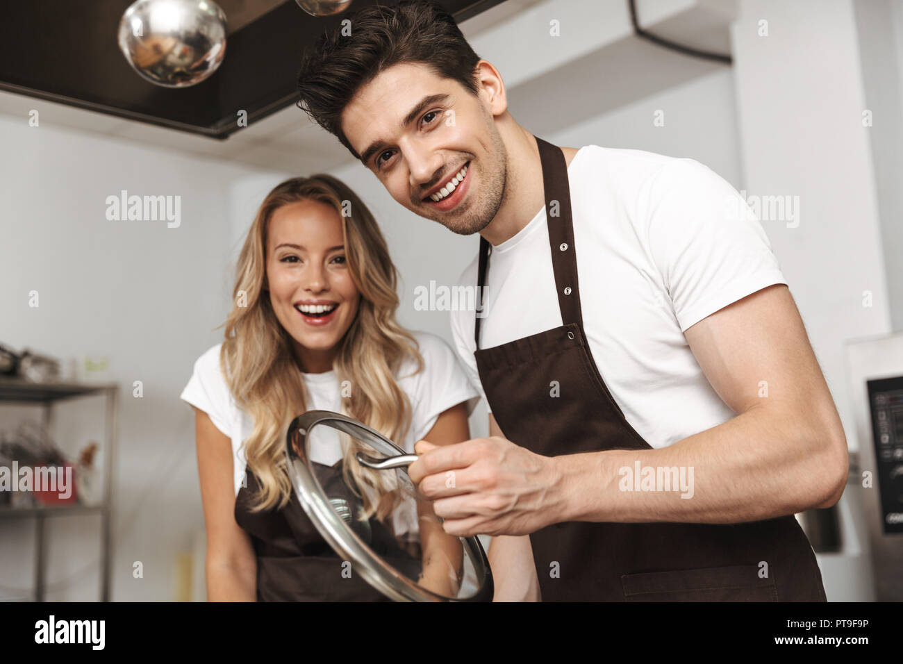 Image of happy young friends loving couple chefs on the kitchen cooking ...