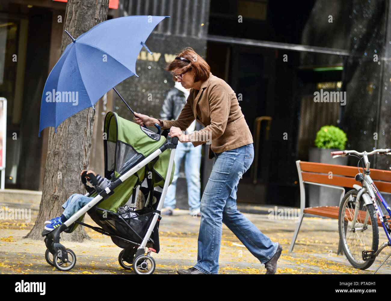 Grandmother carrying her grandson in the rain, usin an umbrella as ...