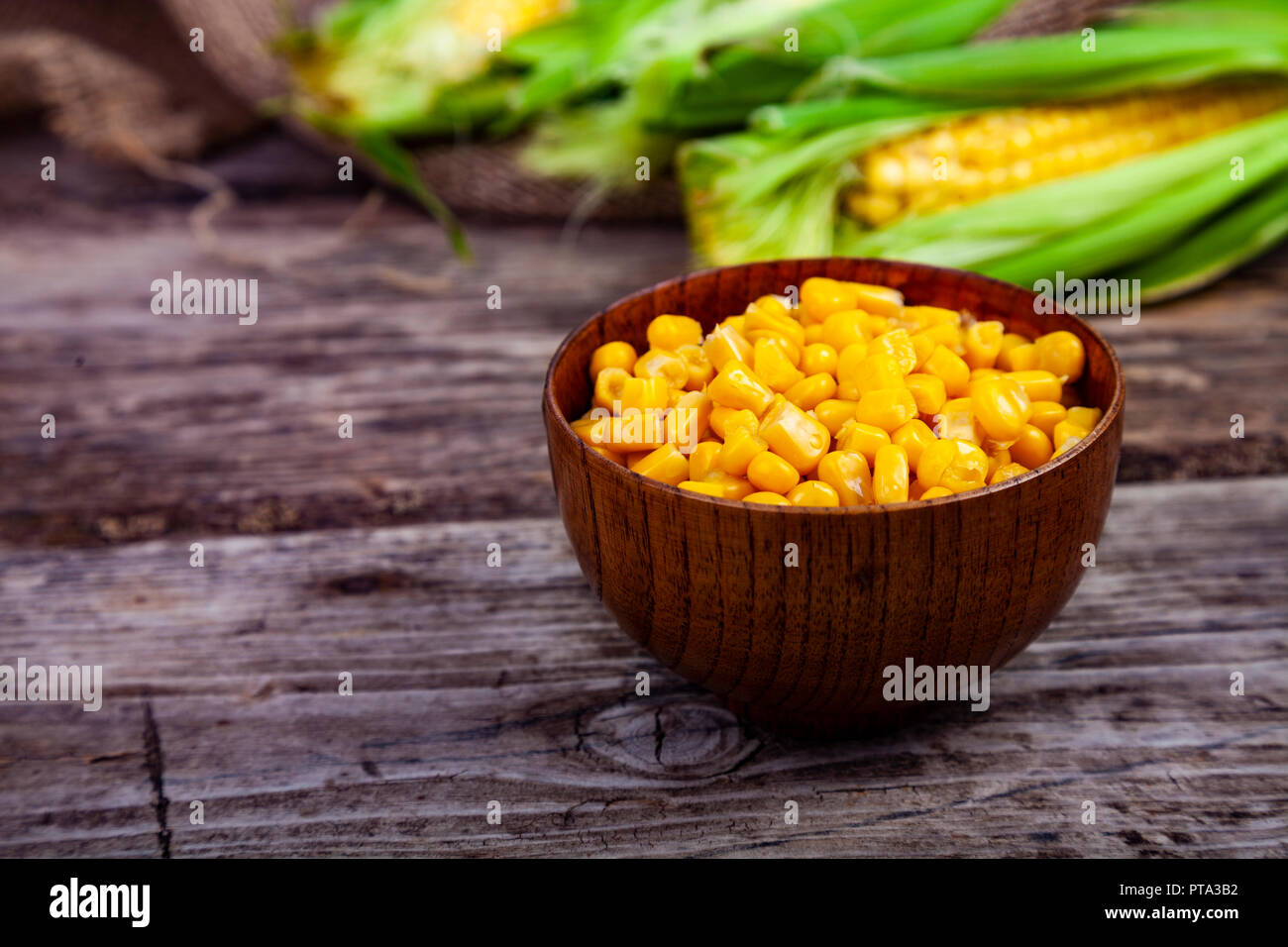 Ripe yellow corn and canned corn in a wooden bowl on a wooden table ...