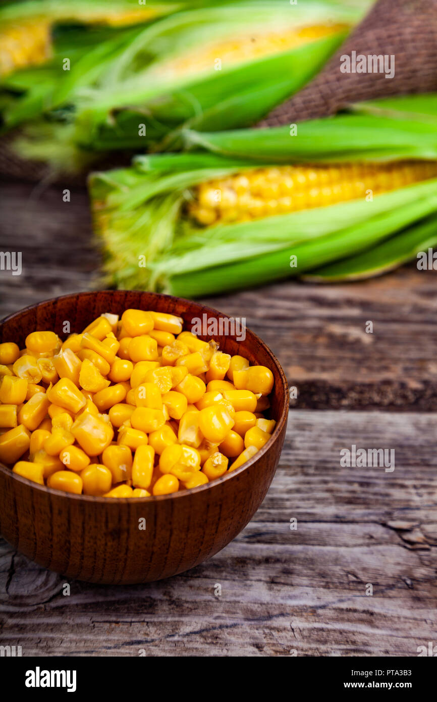 Ripe yellow corn and canned corn in a wooden bowl on a wooden table ...