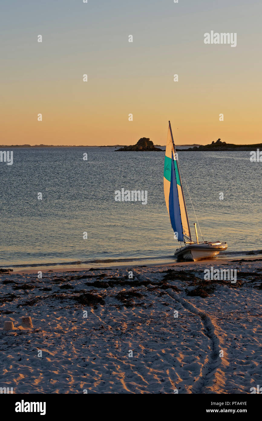 At sunset a small sailing boat rests at the beach at the waters edge ...