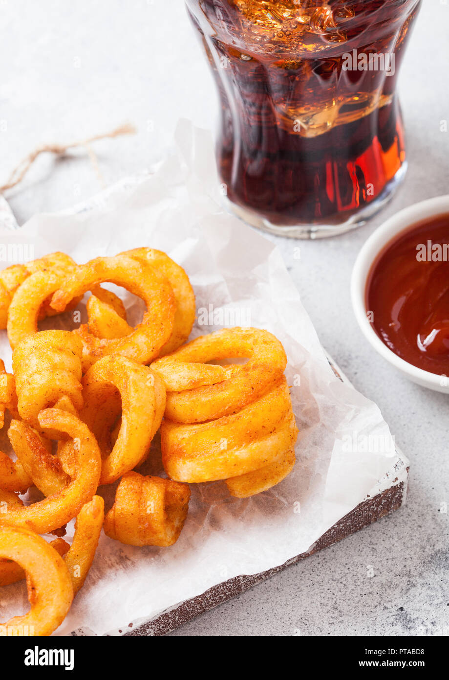 Curly fries fast food snack on wooden board with ketchup and glass of ...