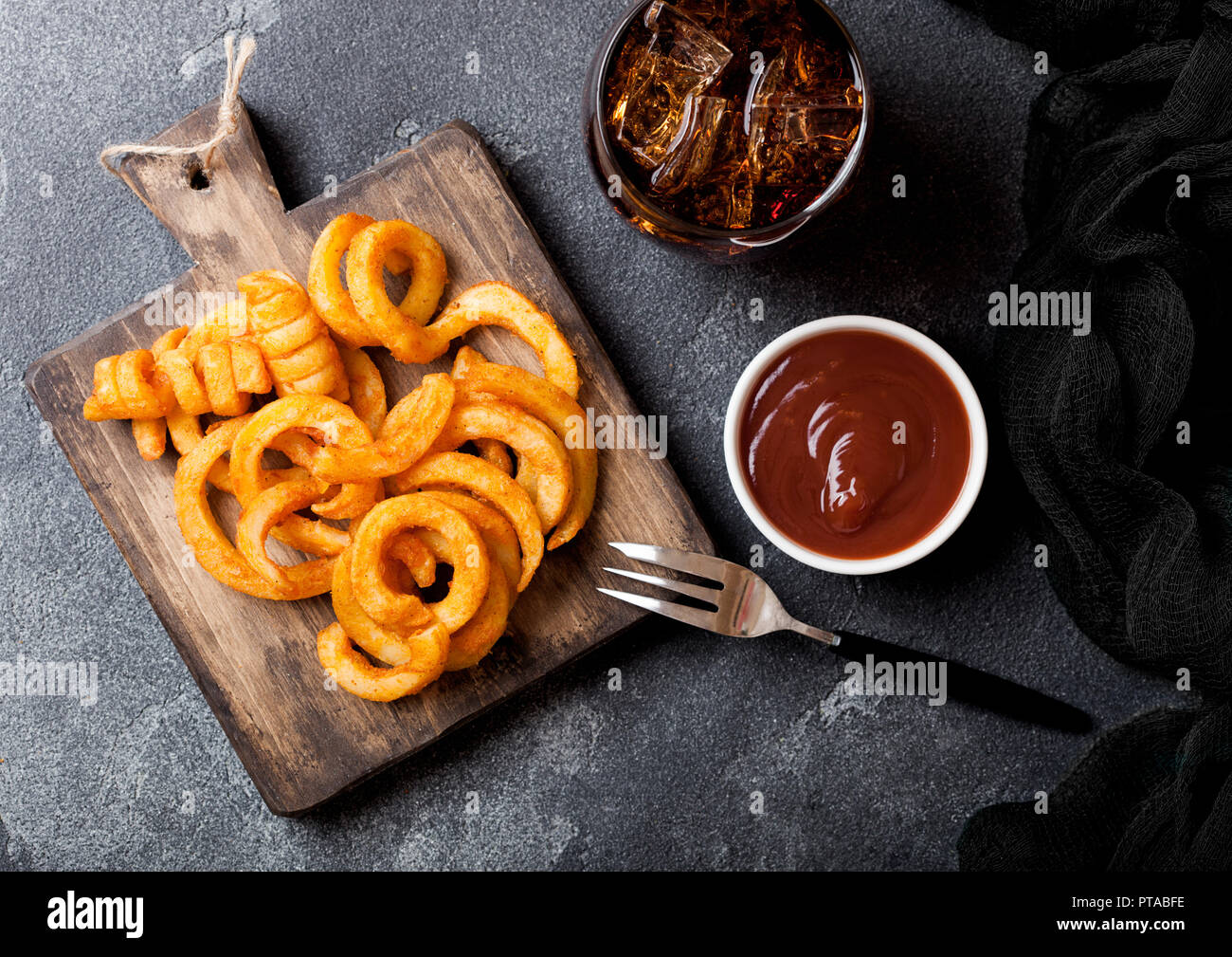 Curly fries fast food snack on wooden board with ketchup and glass of ...