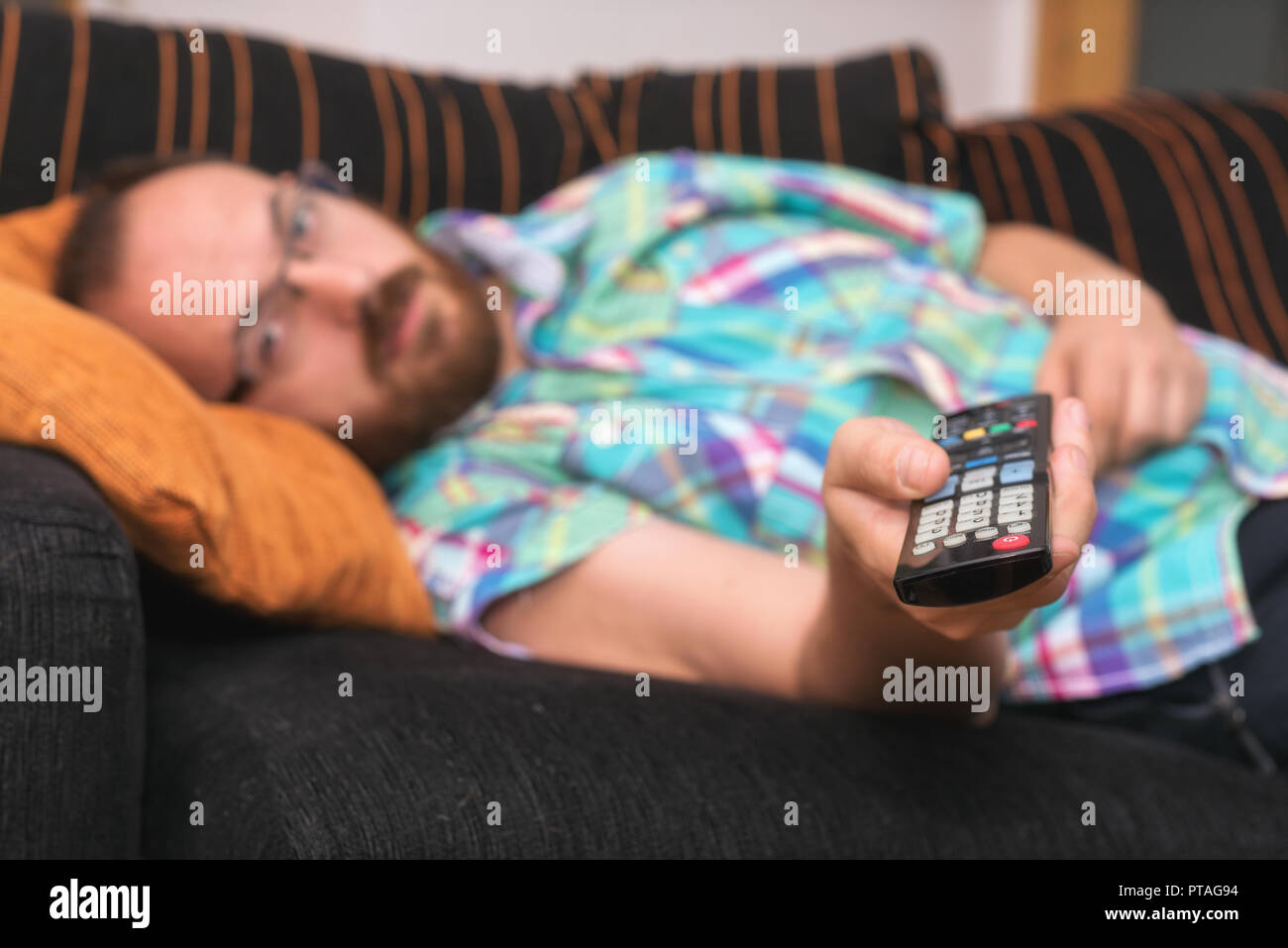 Man relaxing in sofa with remote control watching tv. Shallow dof focus ...