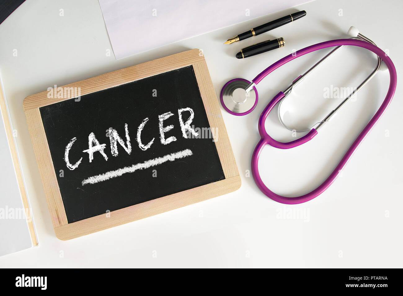 Word CANCER written on a blackboard next to a stethoscope and a pen on ...