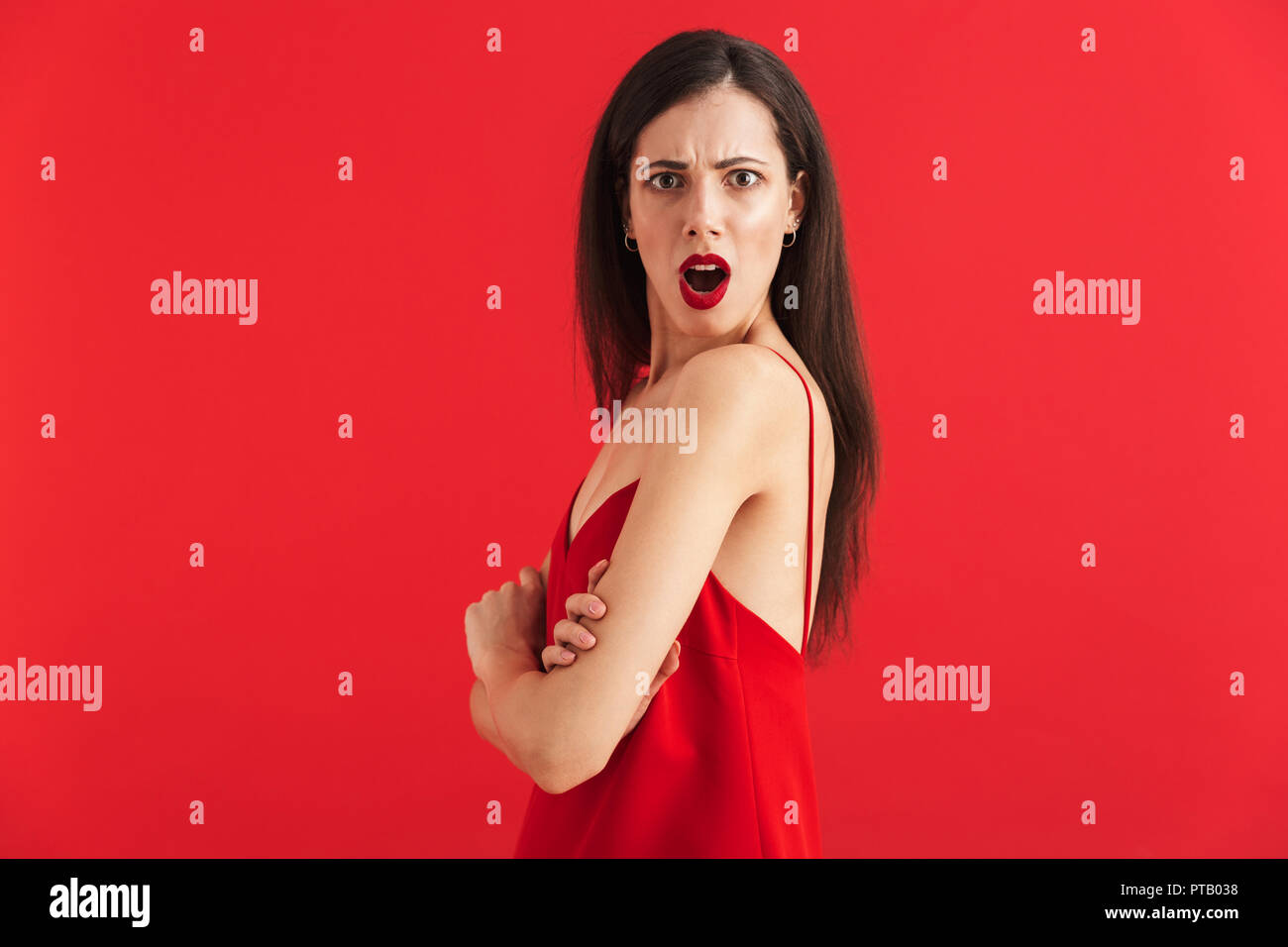 Portrait of an angry young woman in dress isolated over red background ...