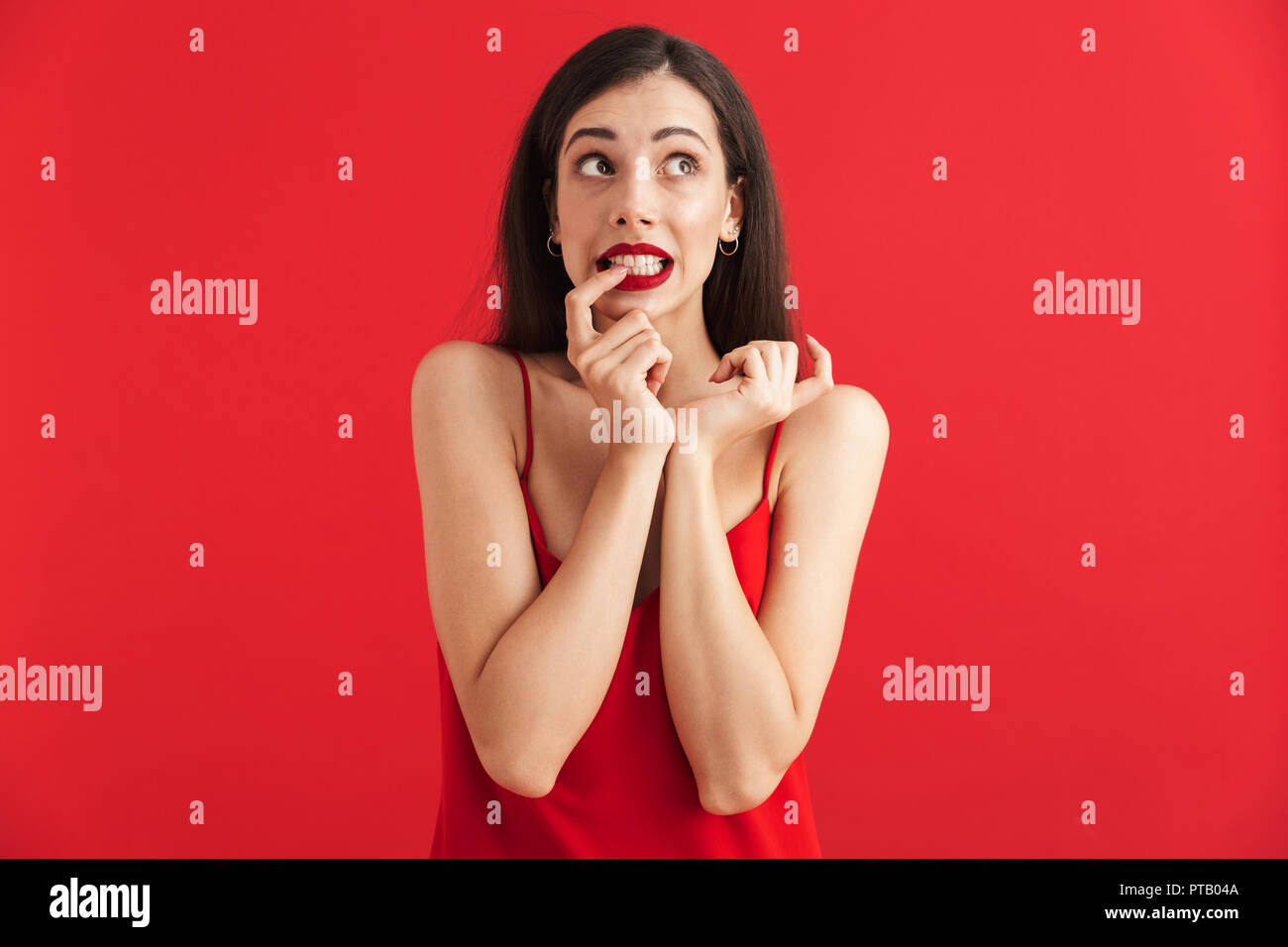 Portrait of a confused young woman in dress isolated over red ...