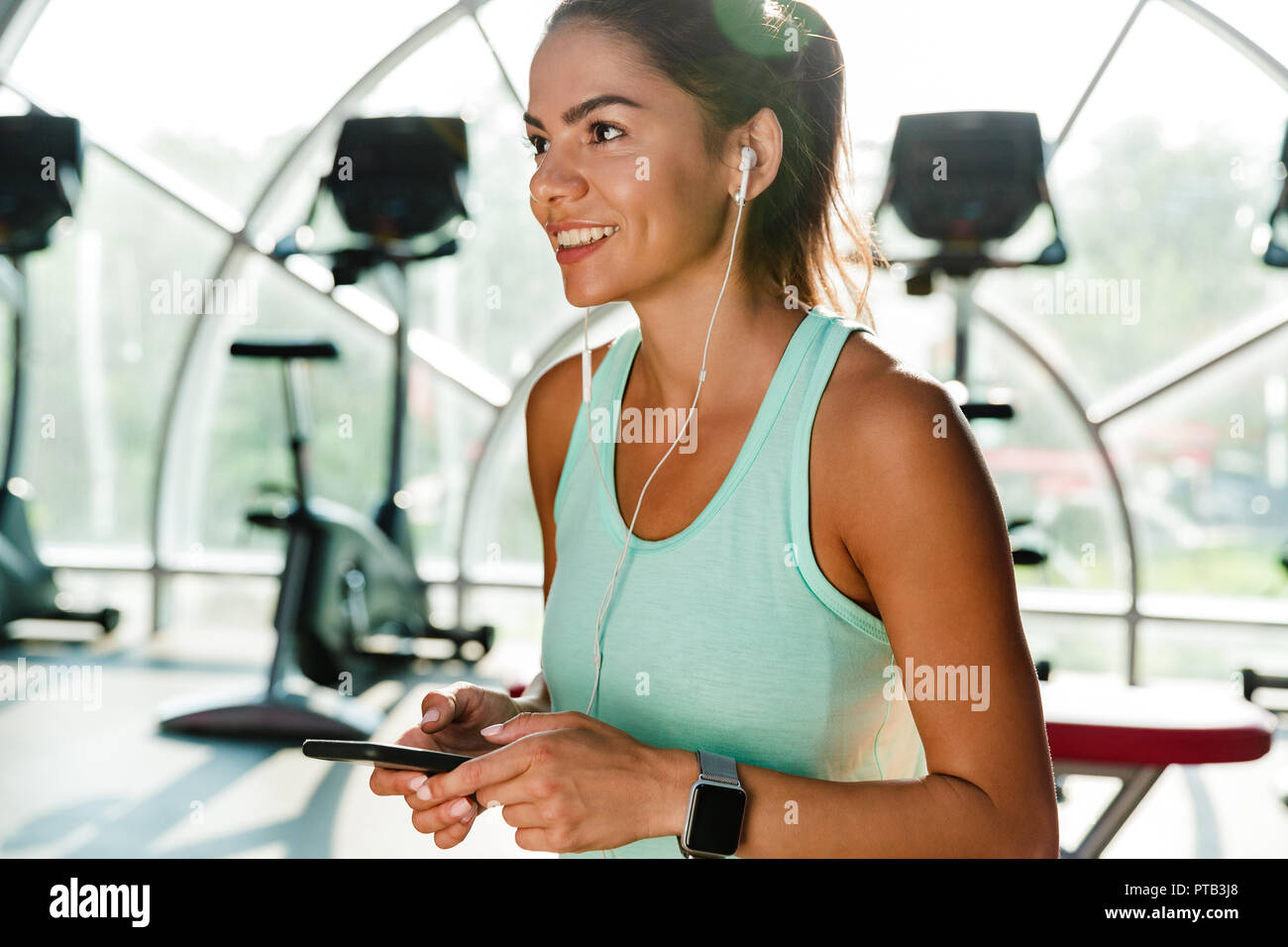 Happy sports woman in earphones holding smartphone and looking away ...