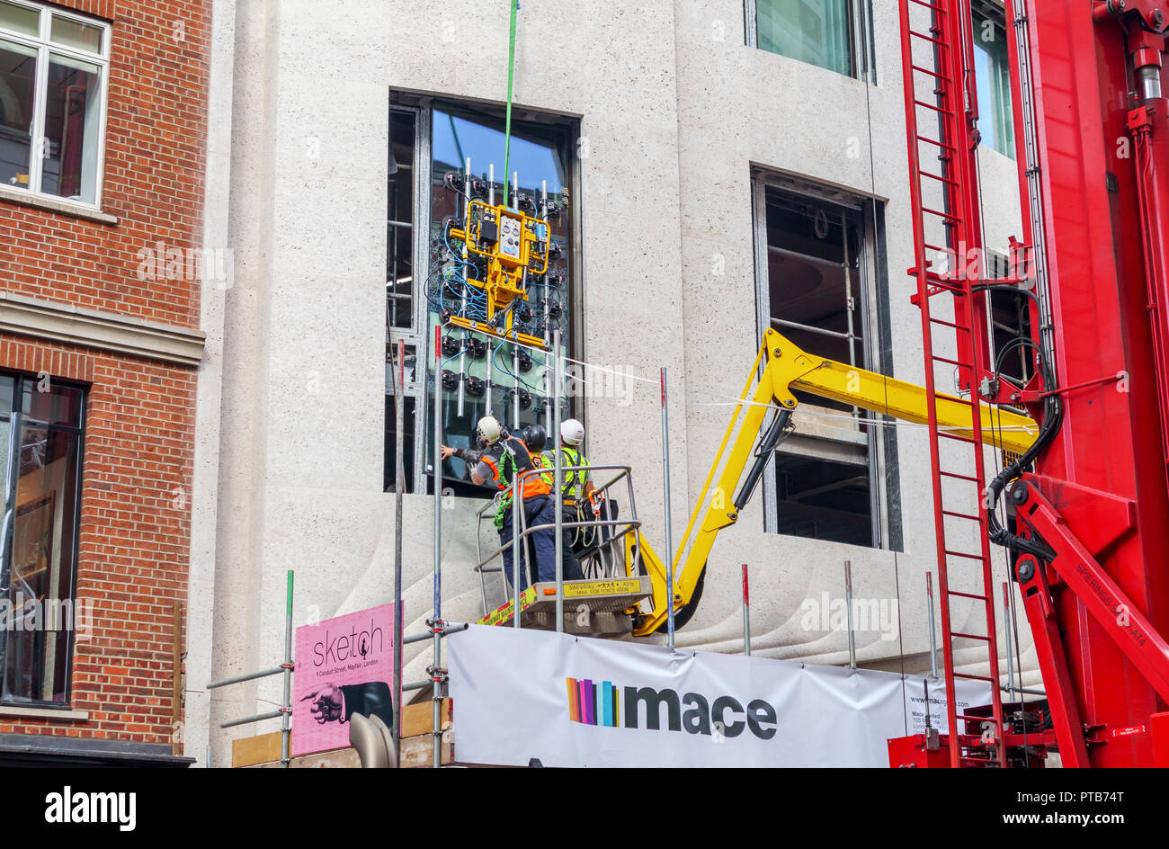 Building contractor Mace workers on a cherry picker hoist carefully ...