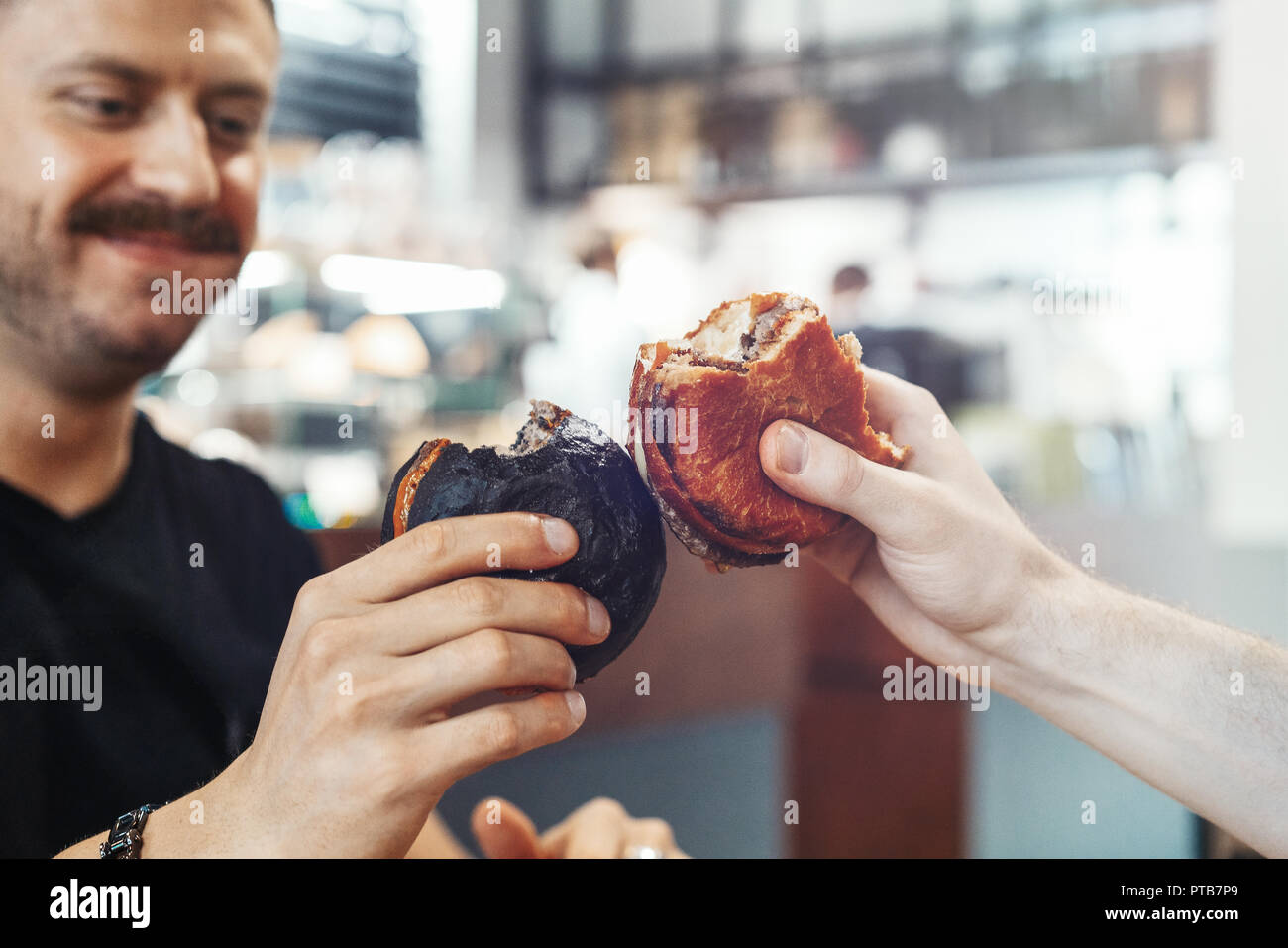 Close up of young handsome man clincing burger at cafe with friend and ...