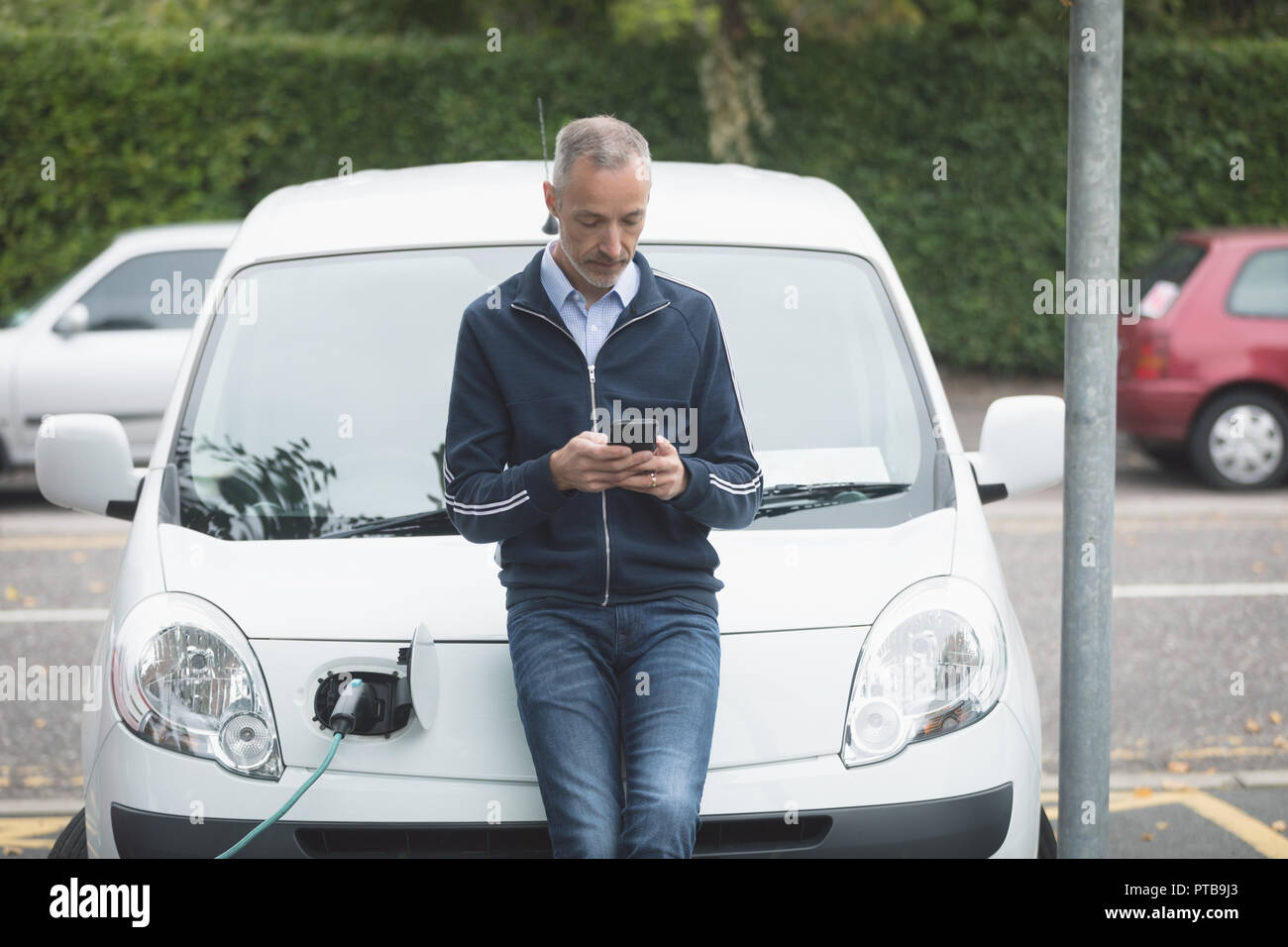 Man using mobile phone while charging electric car Stock Photo - Alamy