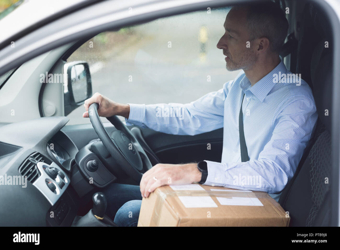 Delivery man with package driving a delivery van Stock Photo - Alamy