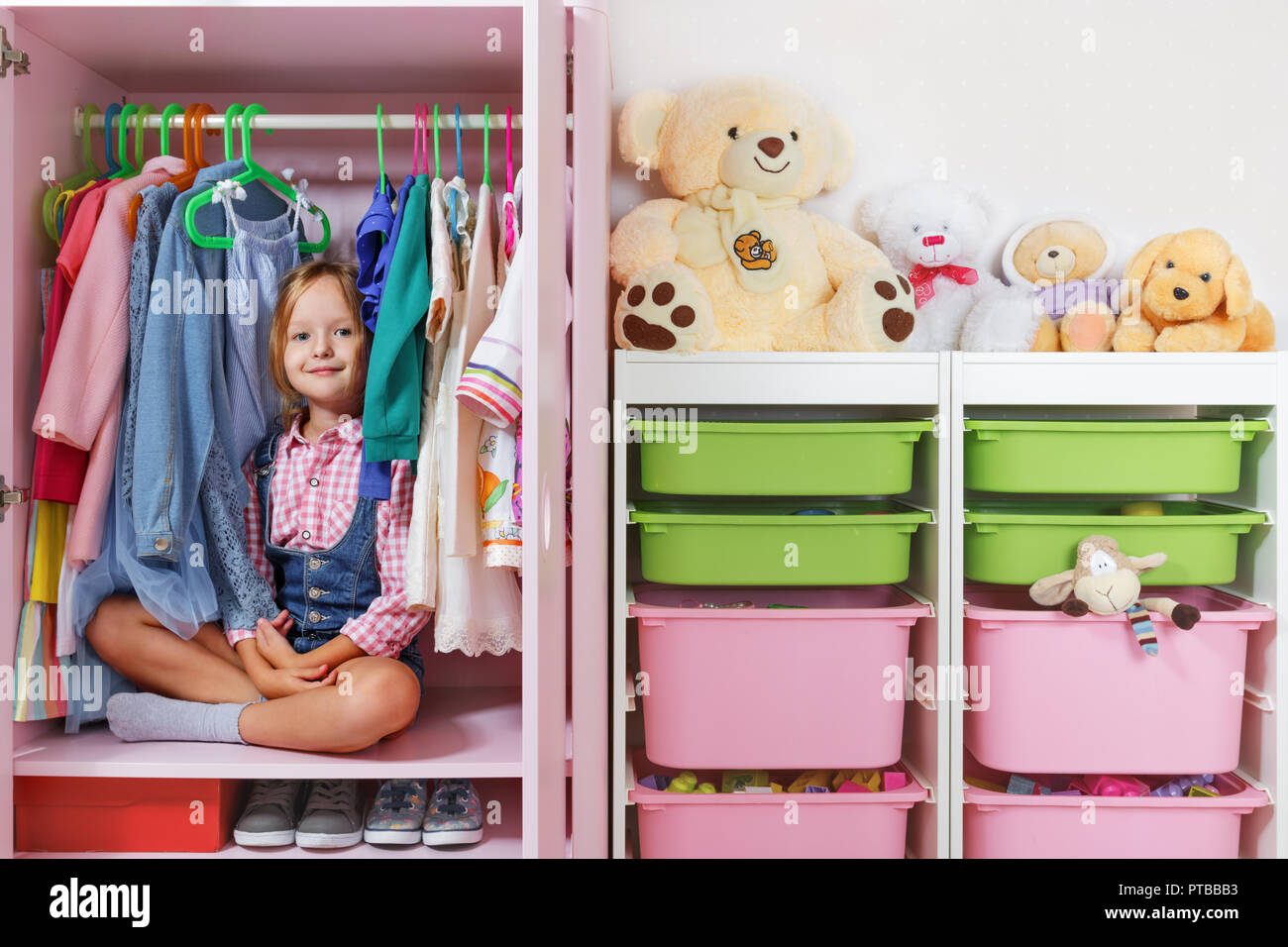 A little child girl is sitting in a wardrobe in a children's room ...