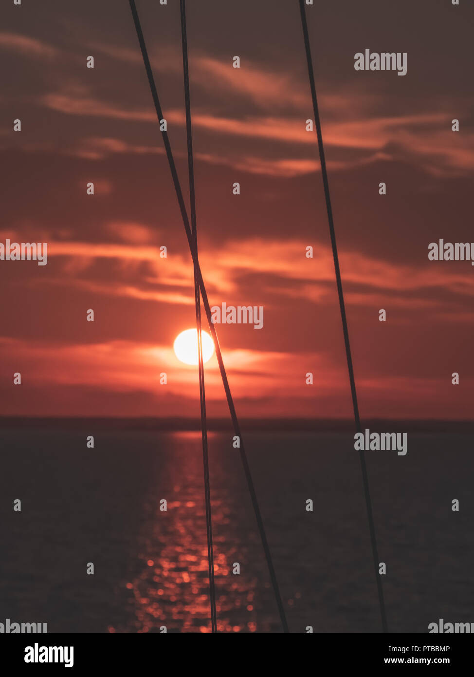 dramatic red sunrise over the baltic sea seen through ships ropes and ...