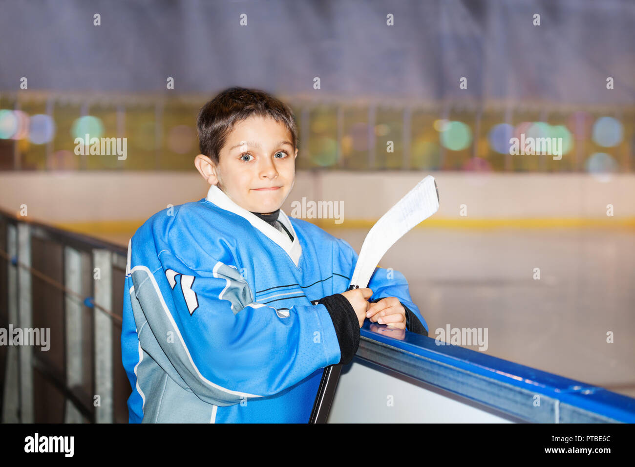 Portrait of happy boy, ice hockey player, standing with stick behind ...