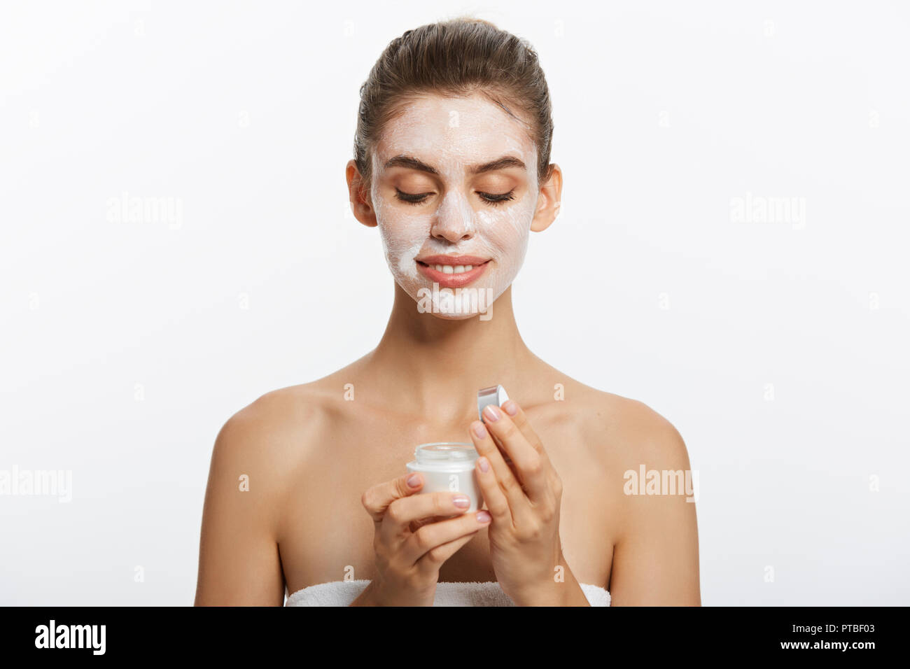 Young woman putting cream on her face isolated on white background ...