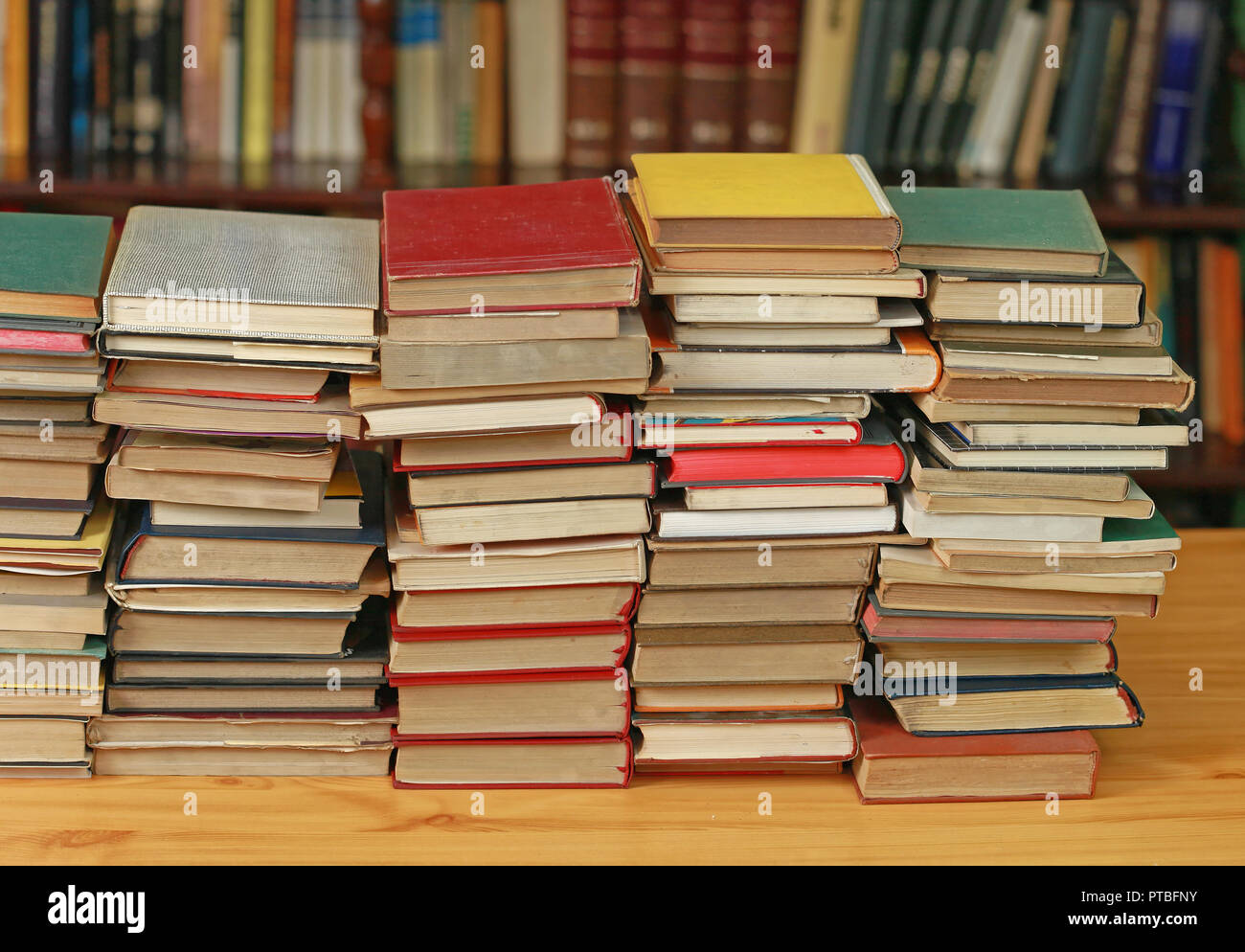 Stacked Books at Desk and Library Shelf in Background Stock Photo - Alamy