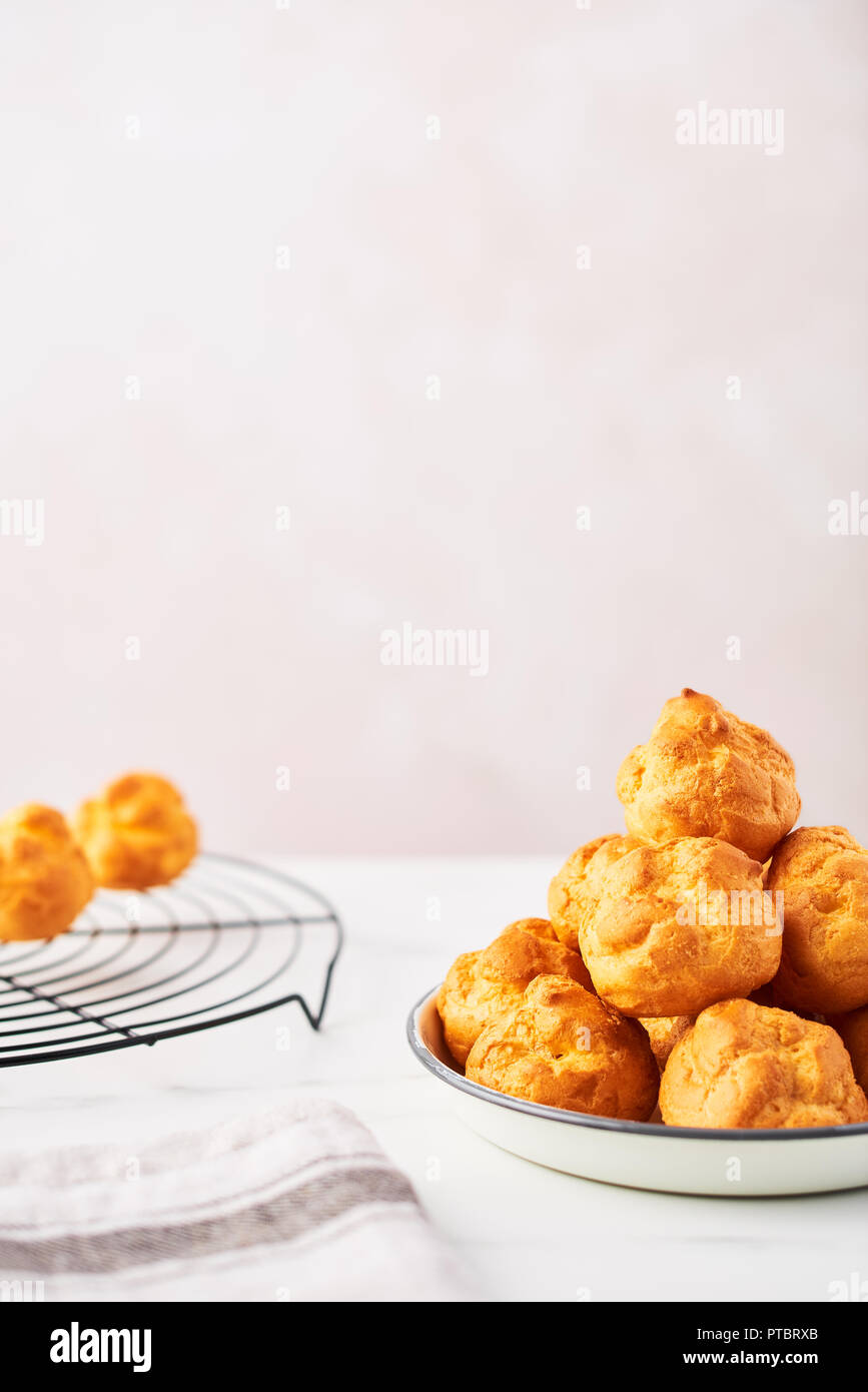 Bunch of fresh cream puff cakes on a white plate and wire rack on white ...