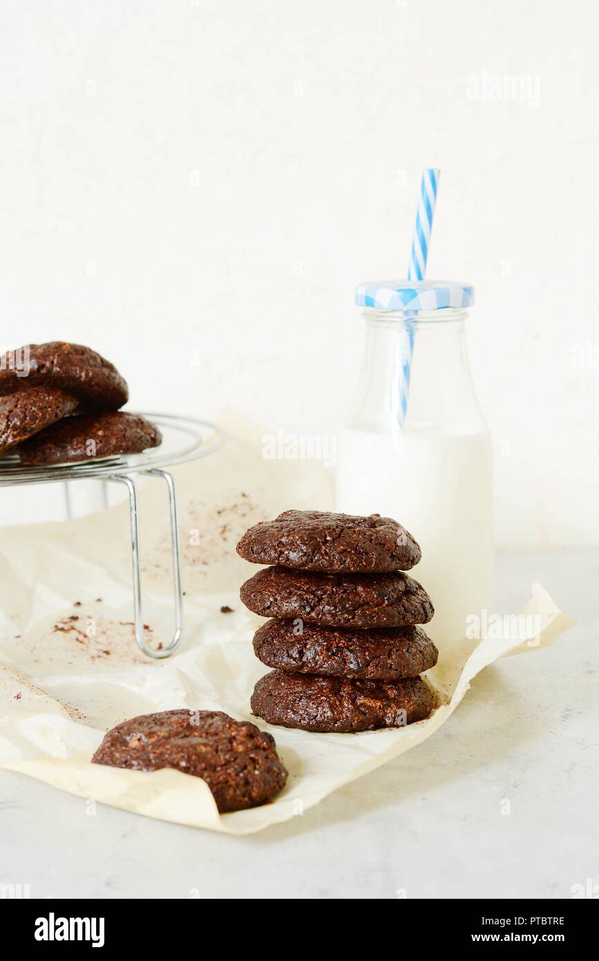 Round baked chocolate biscuits and a bottle of milk on a light ...