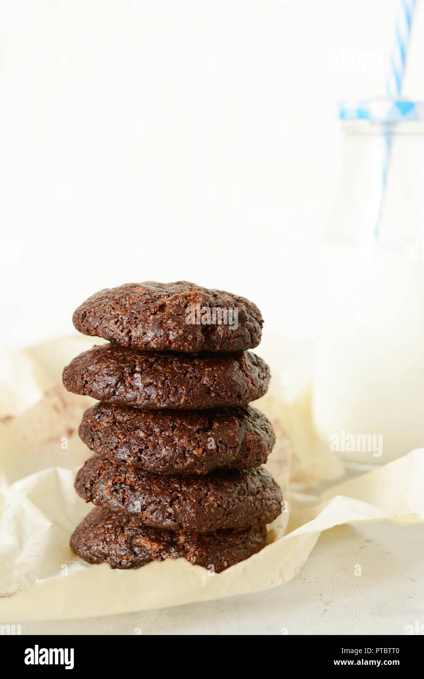 Round baked chocolate biscuits and a bottle of milk on a light ...