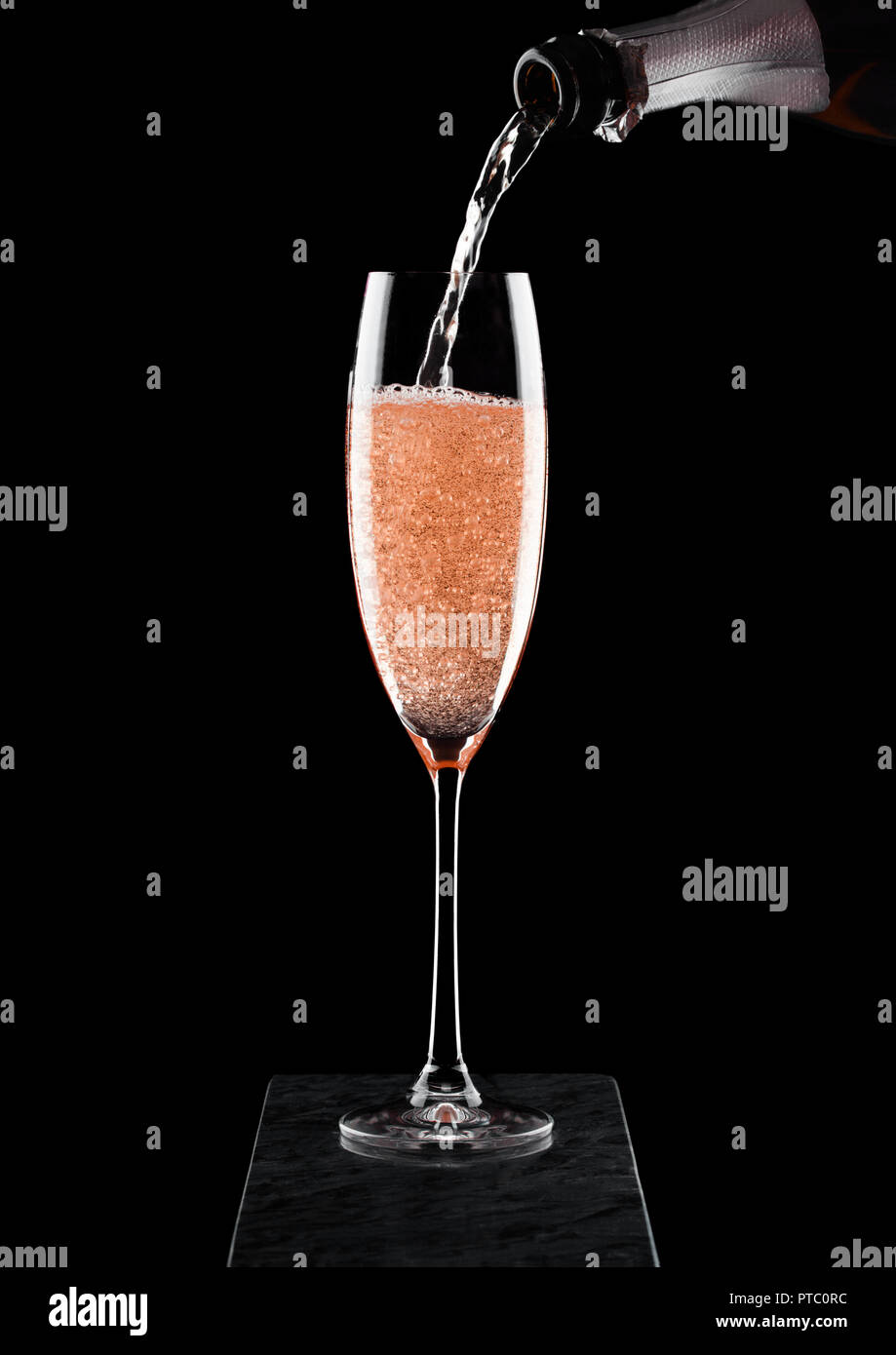 Pouring pink rose champagne from bottle to glass on black marble board ...