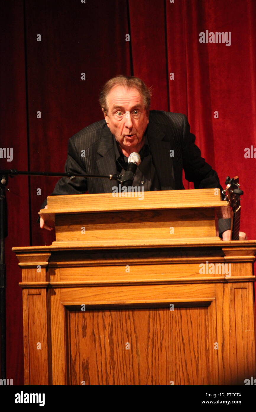 Eric Idle on stage standing at the podium and making a funny concerned ...