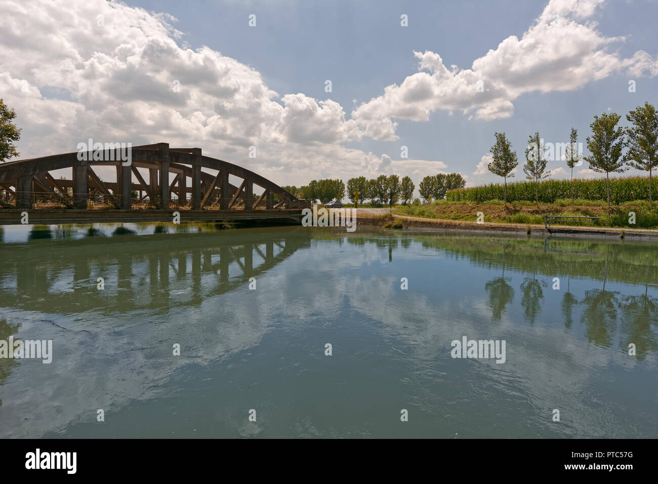 Mirror reflections on the river with bridge, clouds and row of trees ...