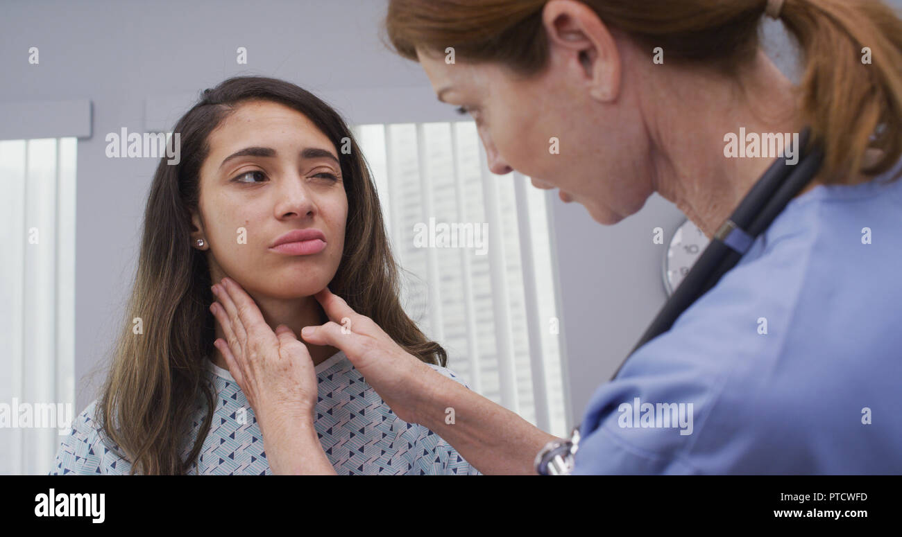 Mid aged nurse comforts young latina patient wearing hospital gown ...