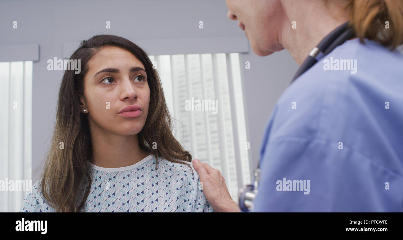 Mid aged nurse comforts young latina patient wearing hospital gown ...