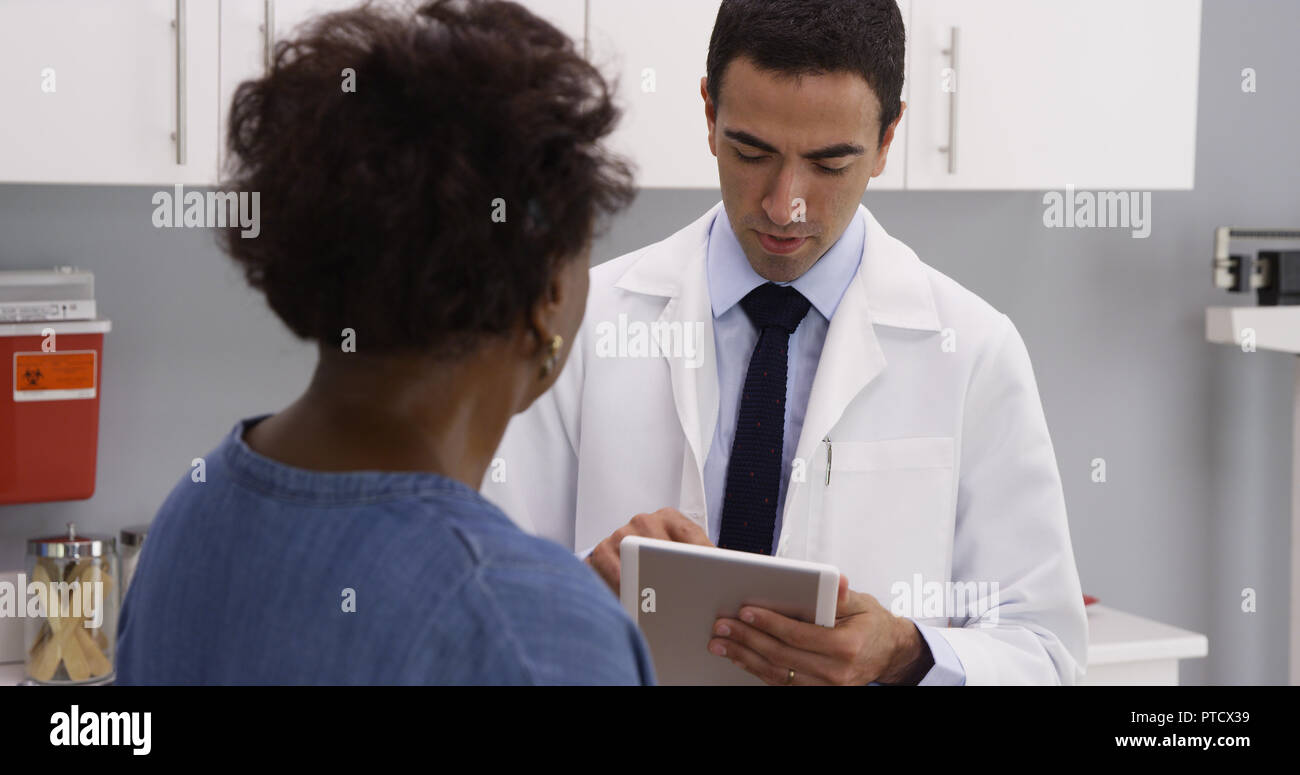 Charming young hispanic doctor using tablet to view patient medical ...