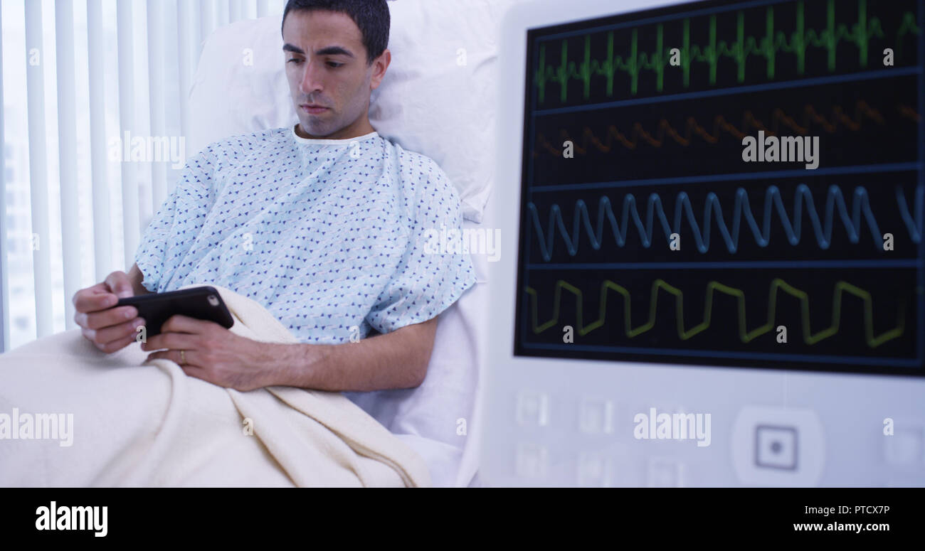 Portrait of charming young male patient using smartphone next to EKG ...